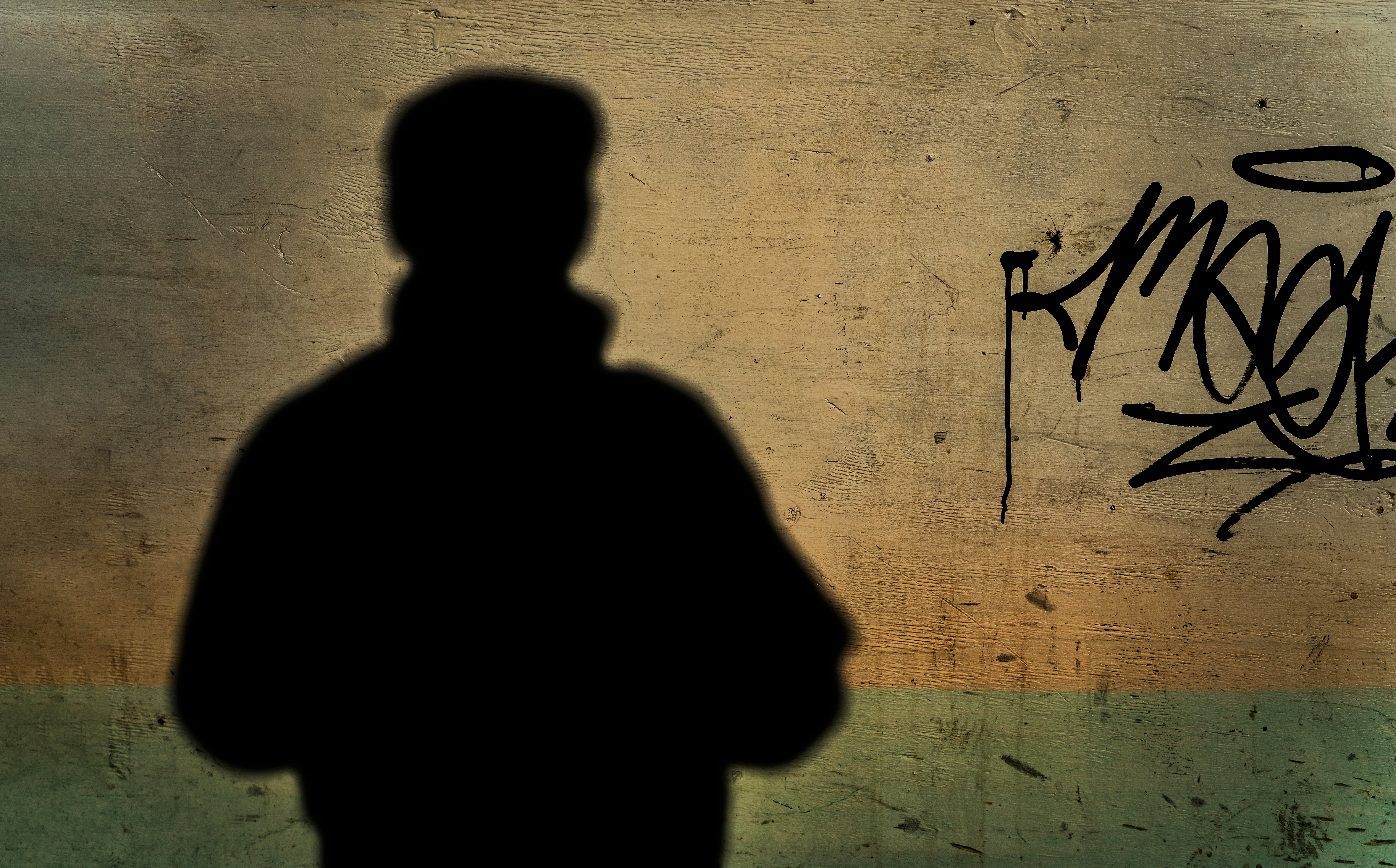 Silhouette of a person against a textured wall with abstract graffiti in earthy tones.