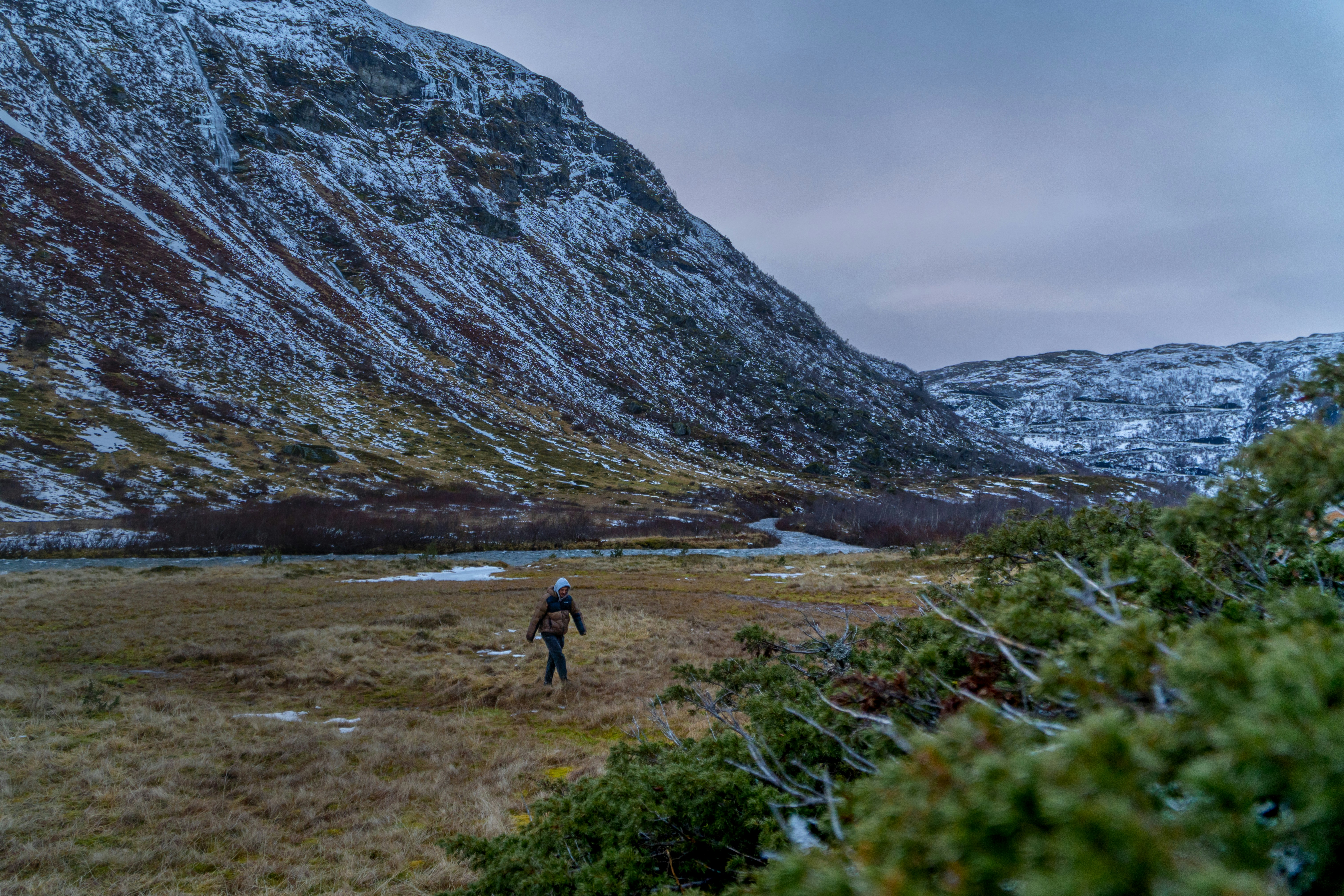 Traveler walks through a snowy valley beneath towering cliffs in Norway.