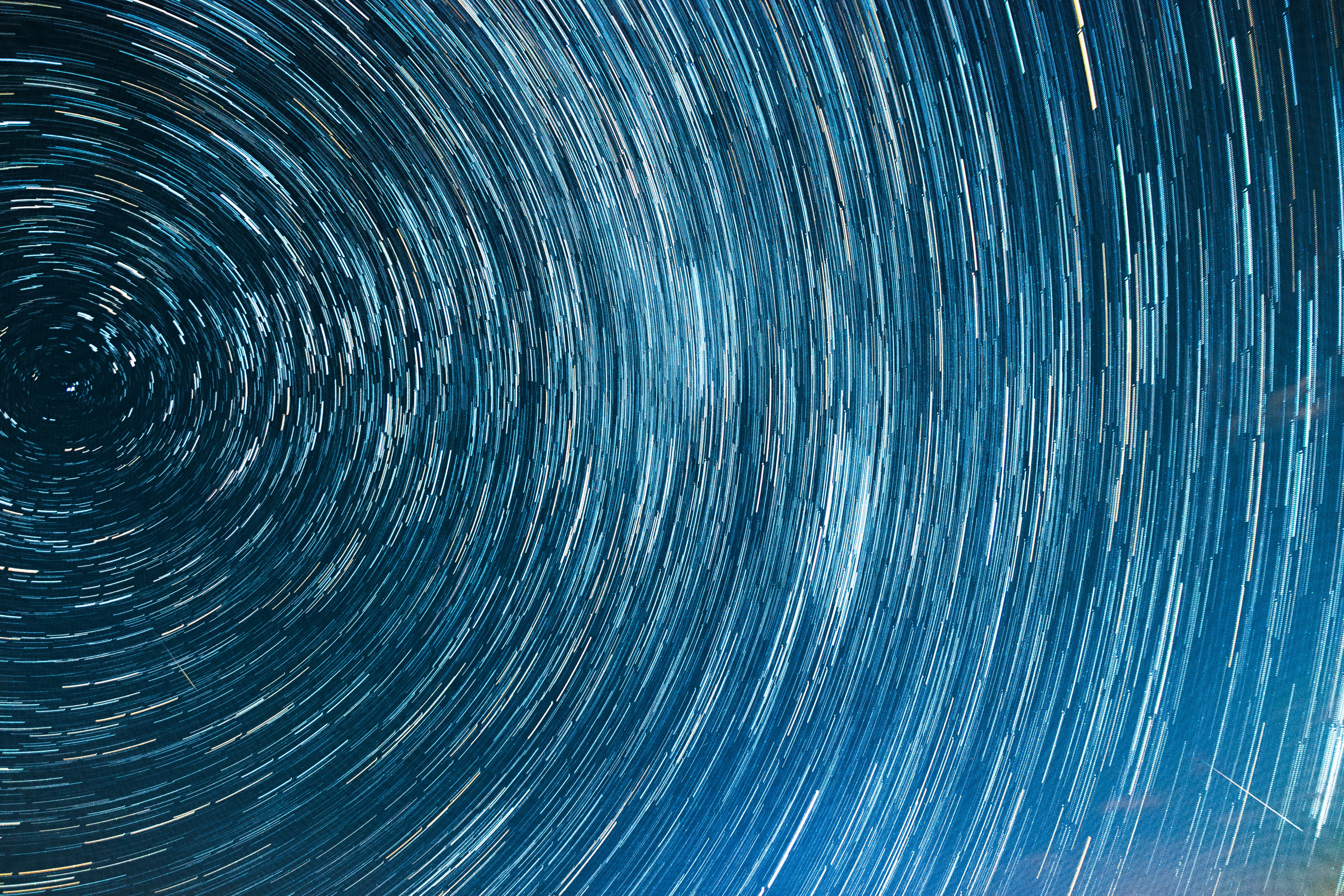 Star trails swirl around the celestial pole in a composite image with blue hues and streaks of light.