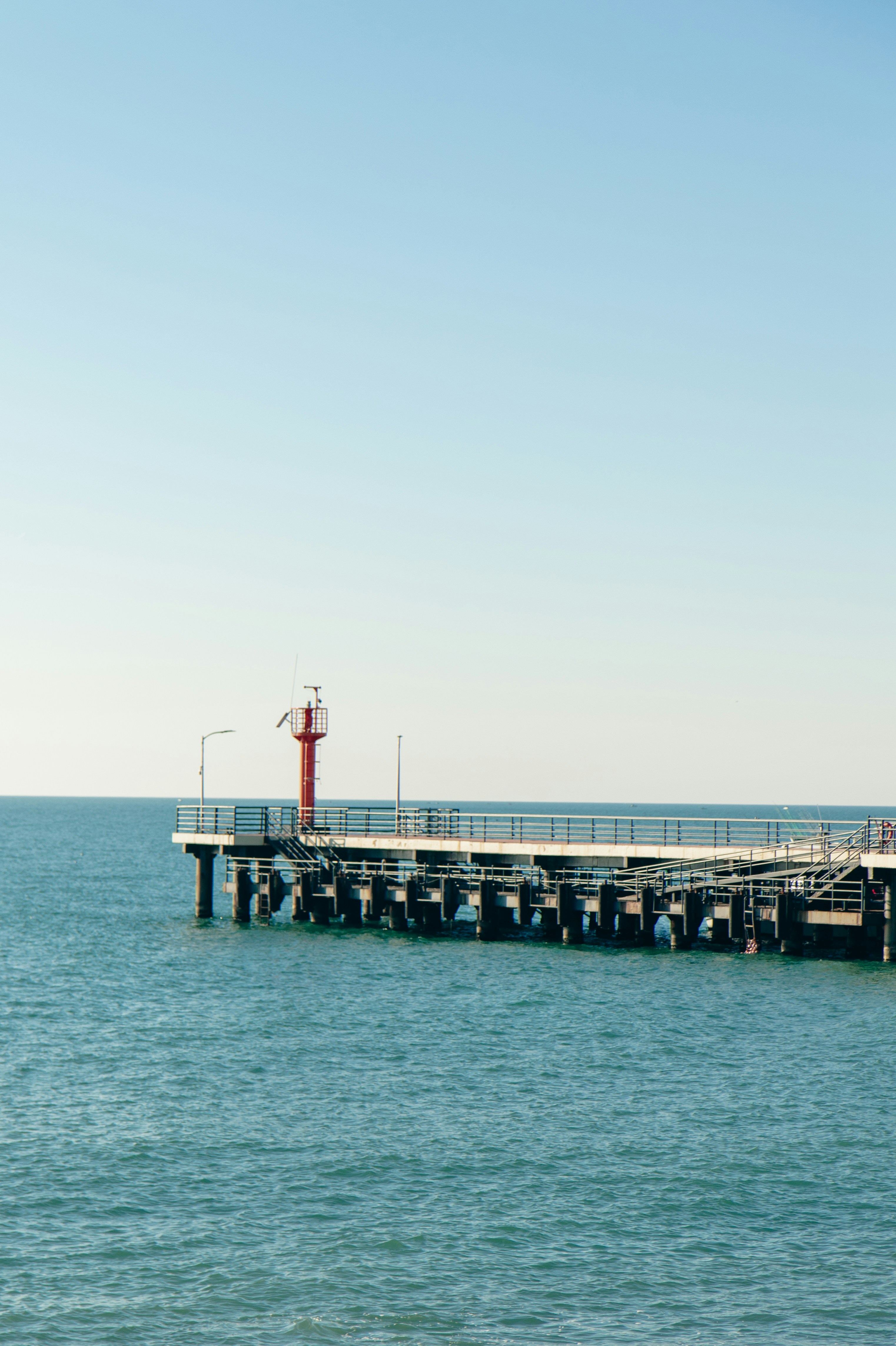 A pier on the ocean with a lighthouse in the distance photo – Free ...