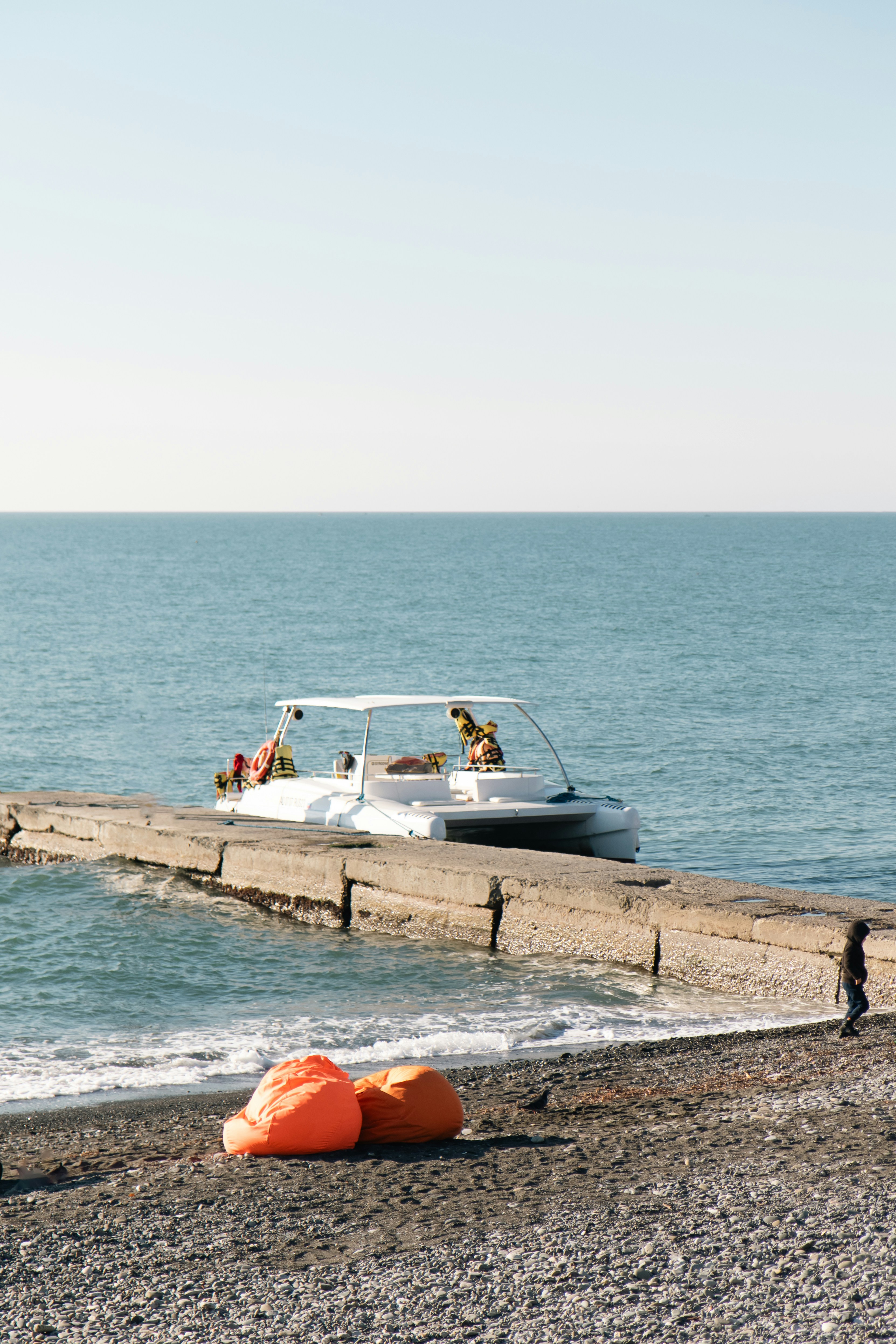 Jetty Rendezvous: A White Motorboat Tied to a Stone Breakwater with Pebbled Foreground