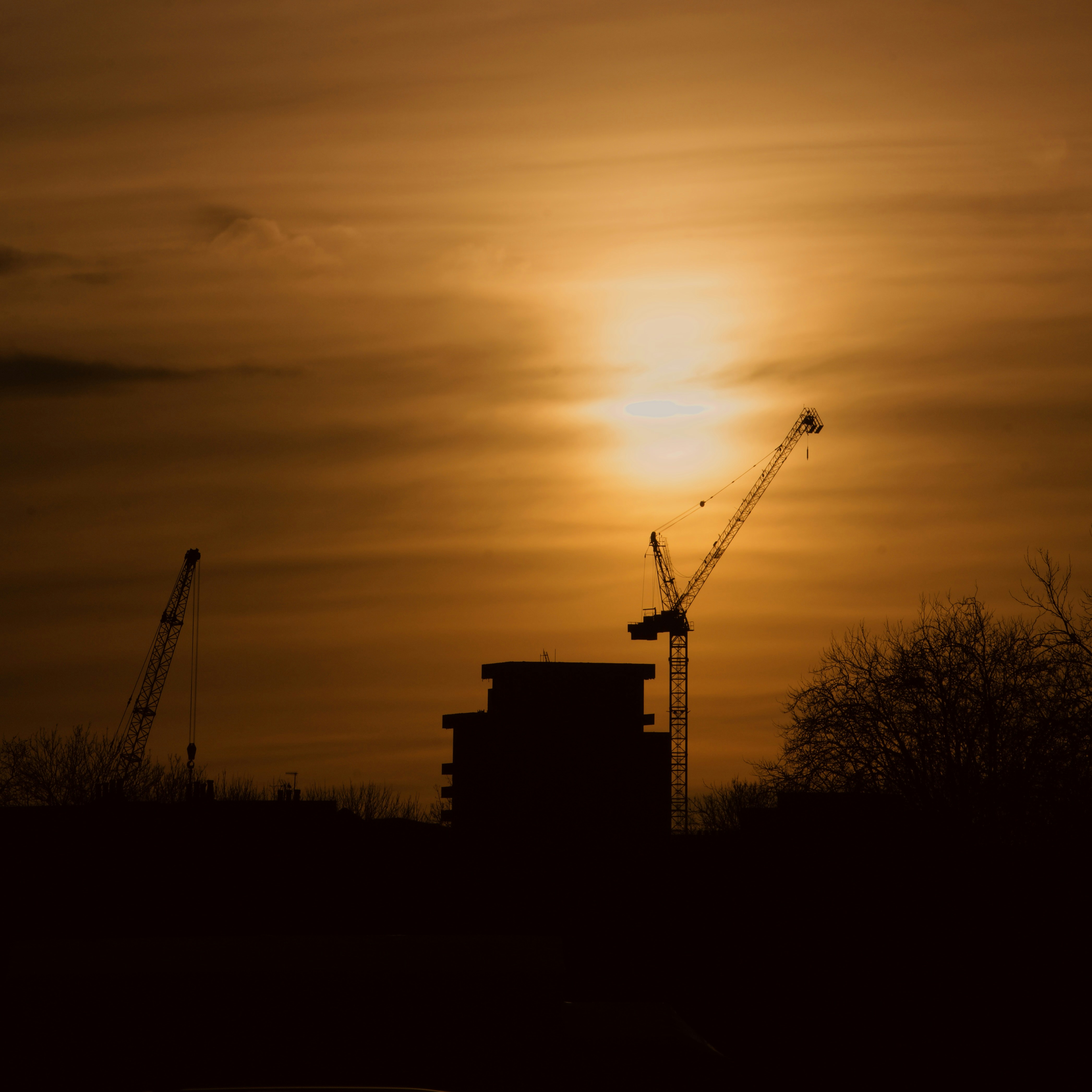 Crane Silhouettes Against a Molten Sunset Over a Quiet Construction Horizon