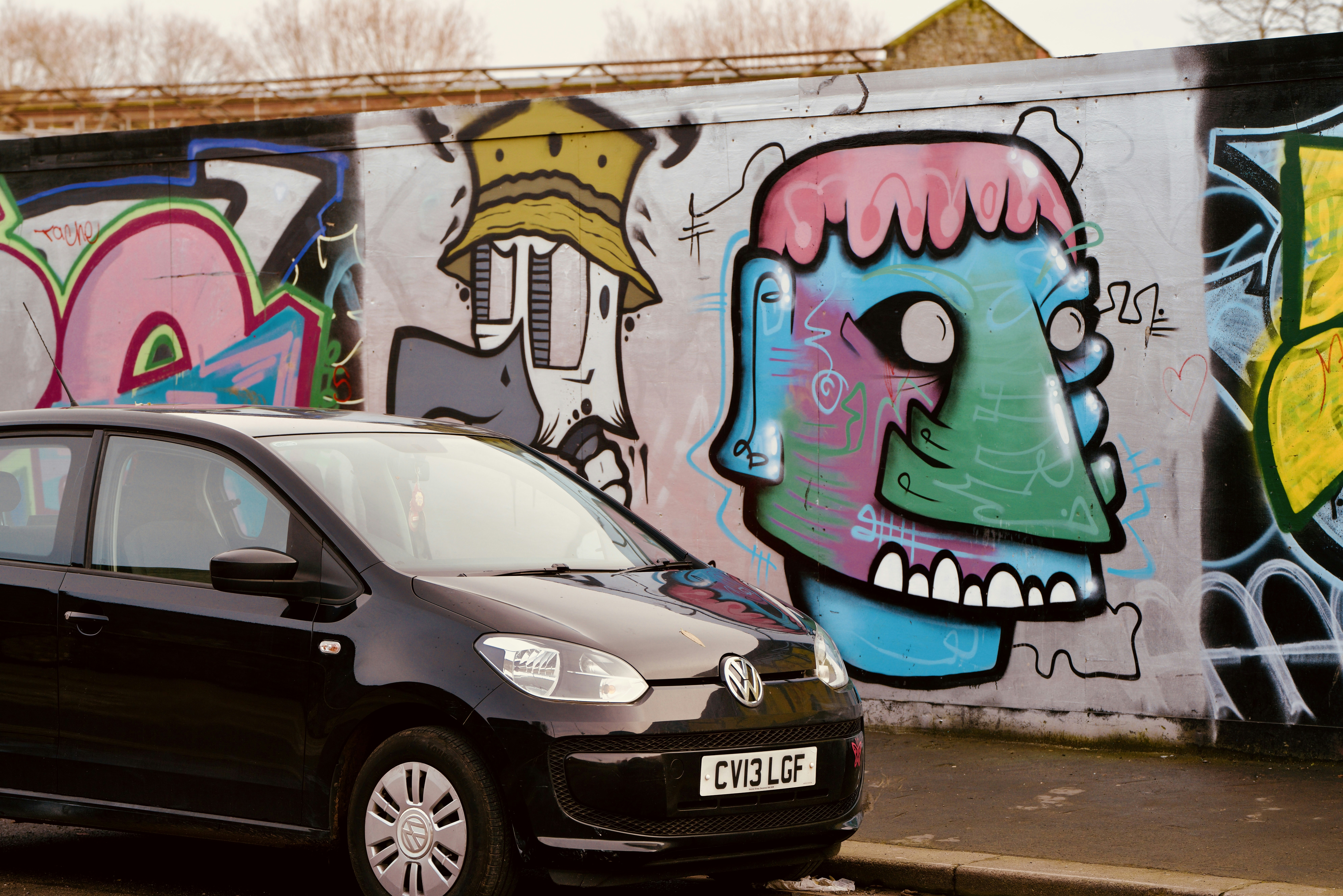 Black Volkswagen parked beside graffiti wall featuring colorful, exaggerated faces.