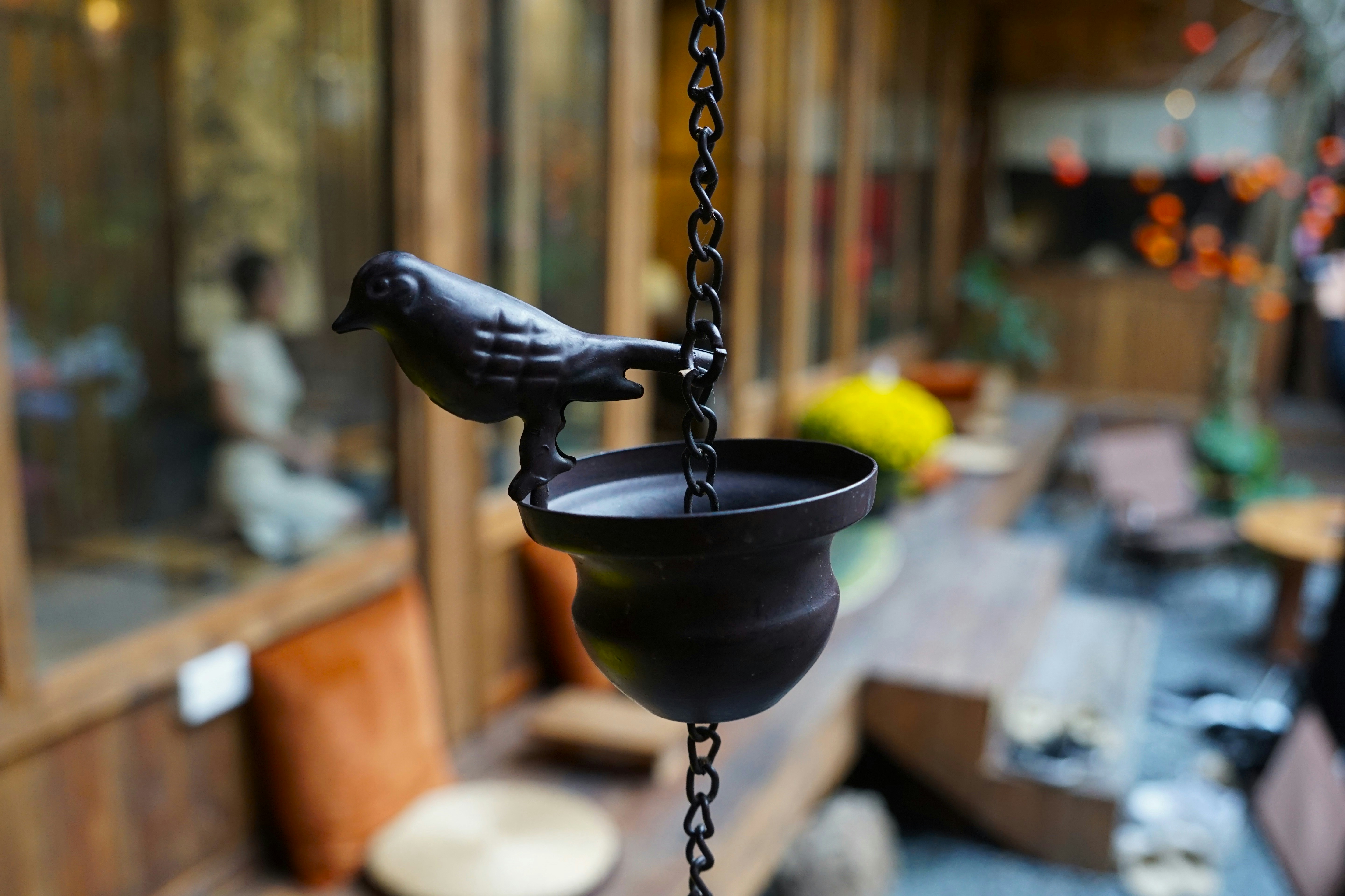 A Bird-Shaped Feeder Perches Above a Hanging Cup in a Cozy Café Courtyard