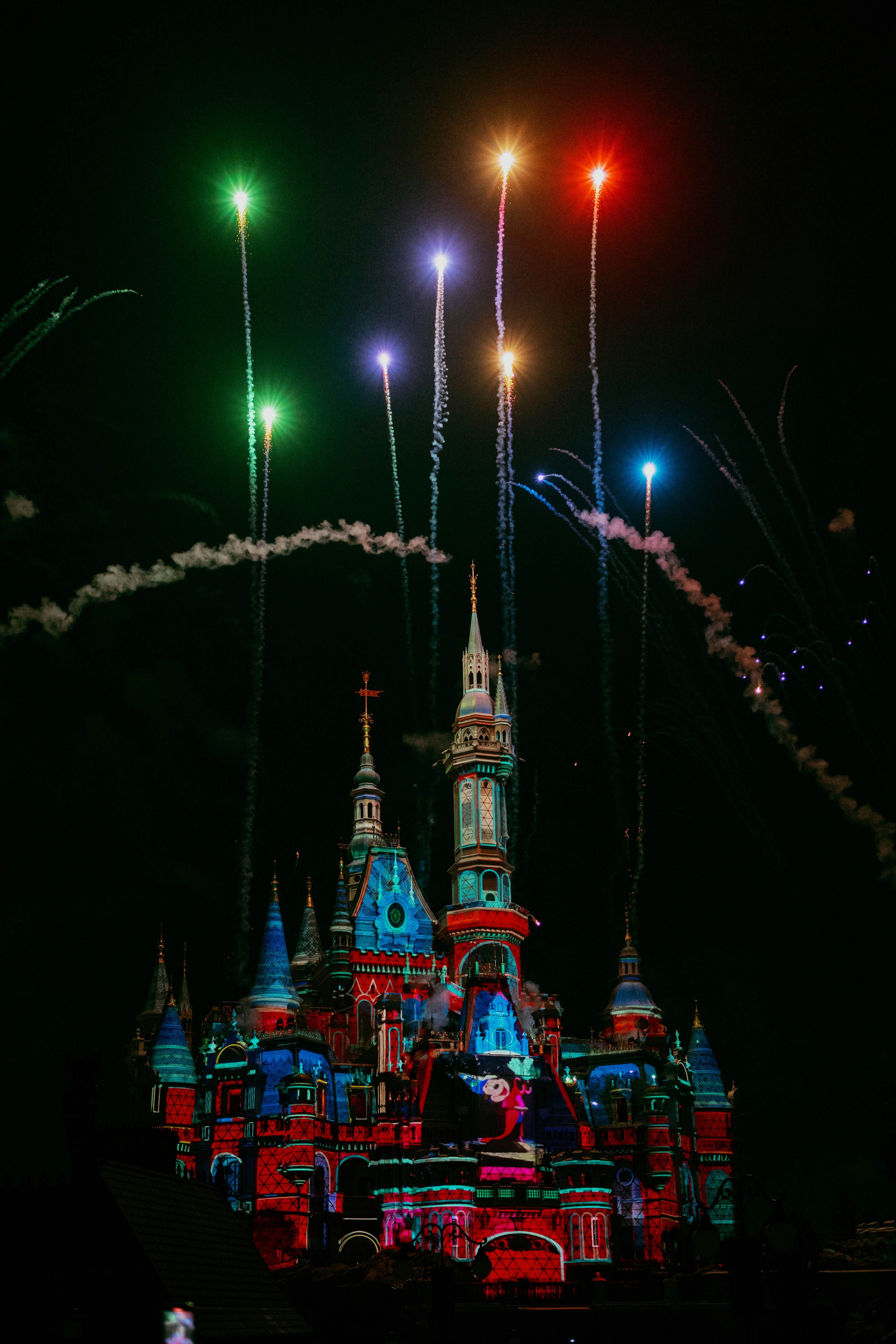 Vibrant fireworks illuminate a fairytale castle, showcasing intricate projections against a night sky. The scene captures the magic of a festive celebration.