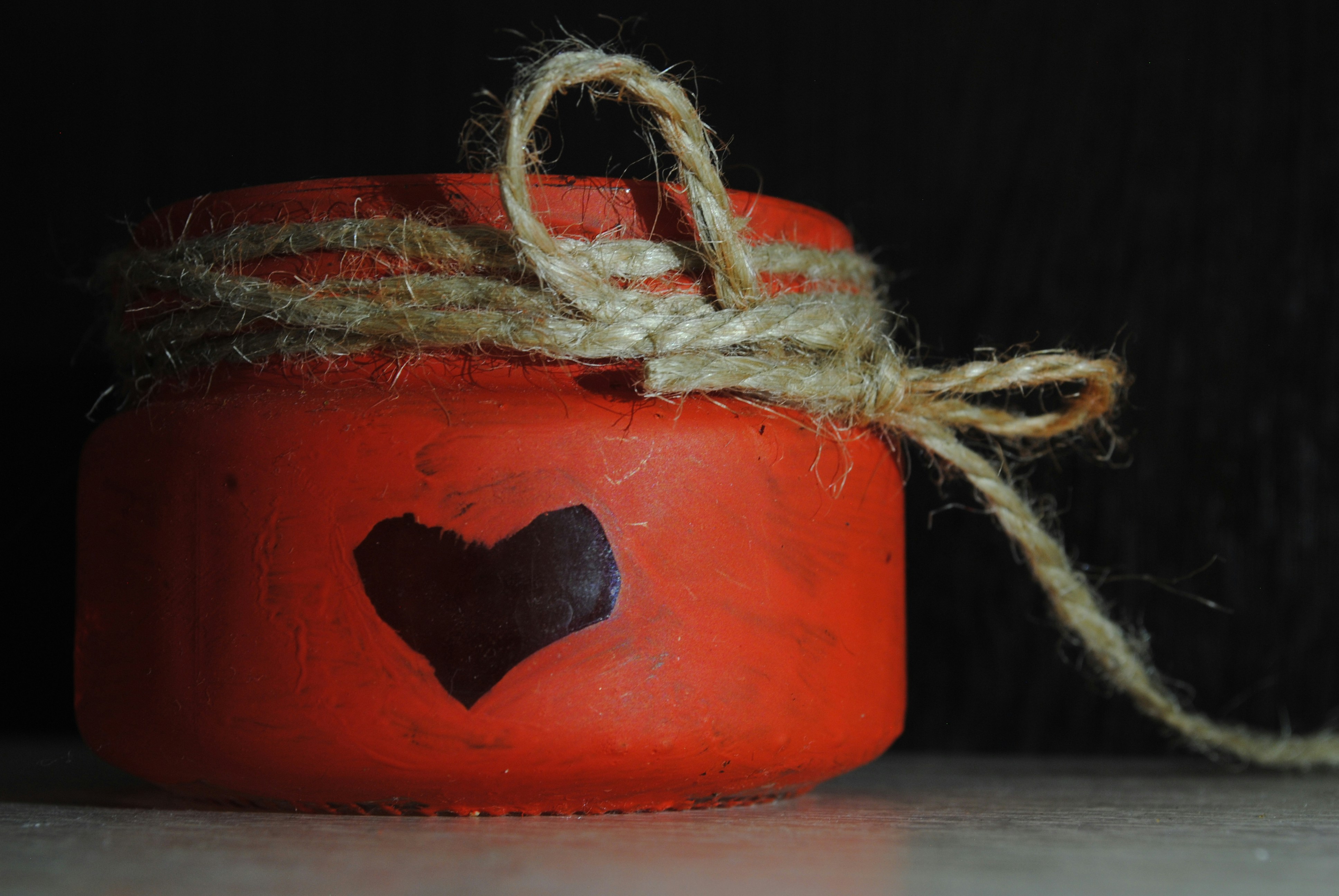 Handcrafted orange clay jar adorned with natural twine and a heart motif, set against a dark background.