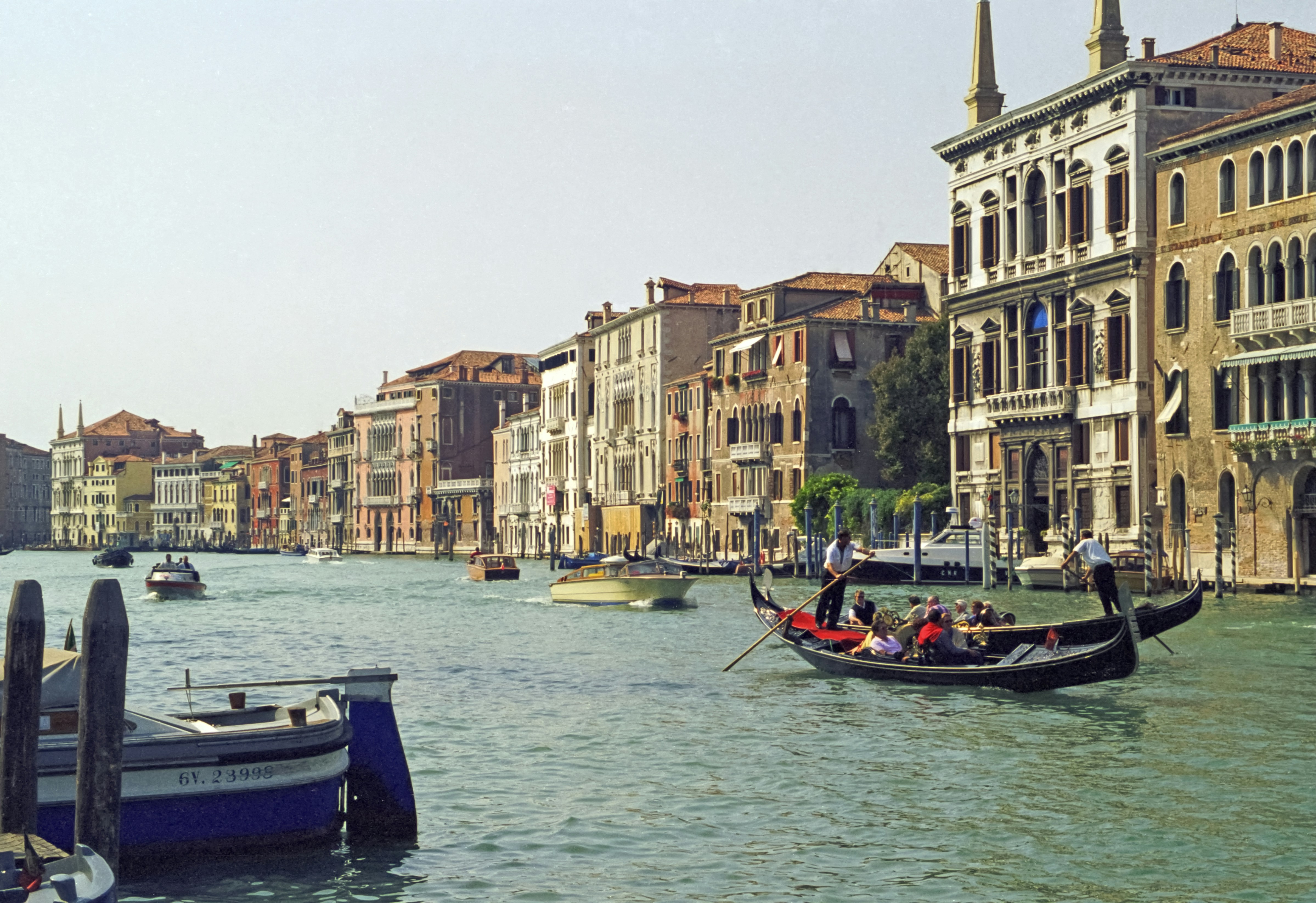Gondolas and boats navigate the bustling Grand Canal in Venice under a clear sky.
