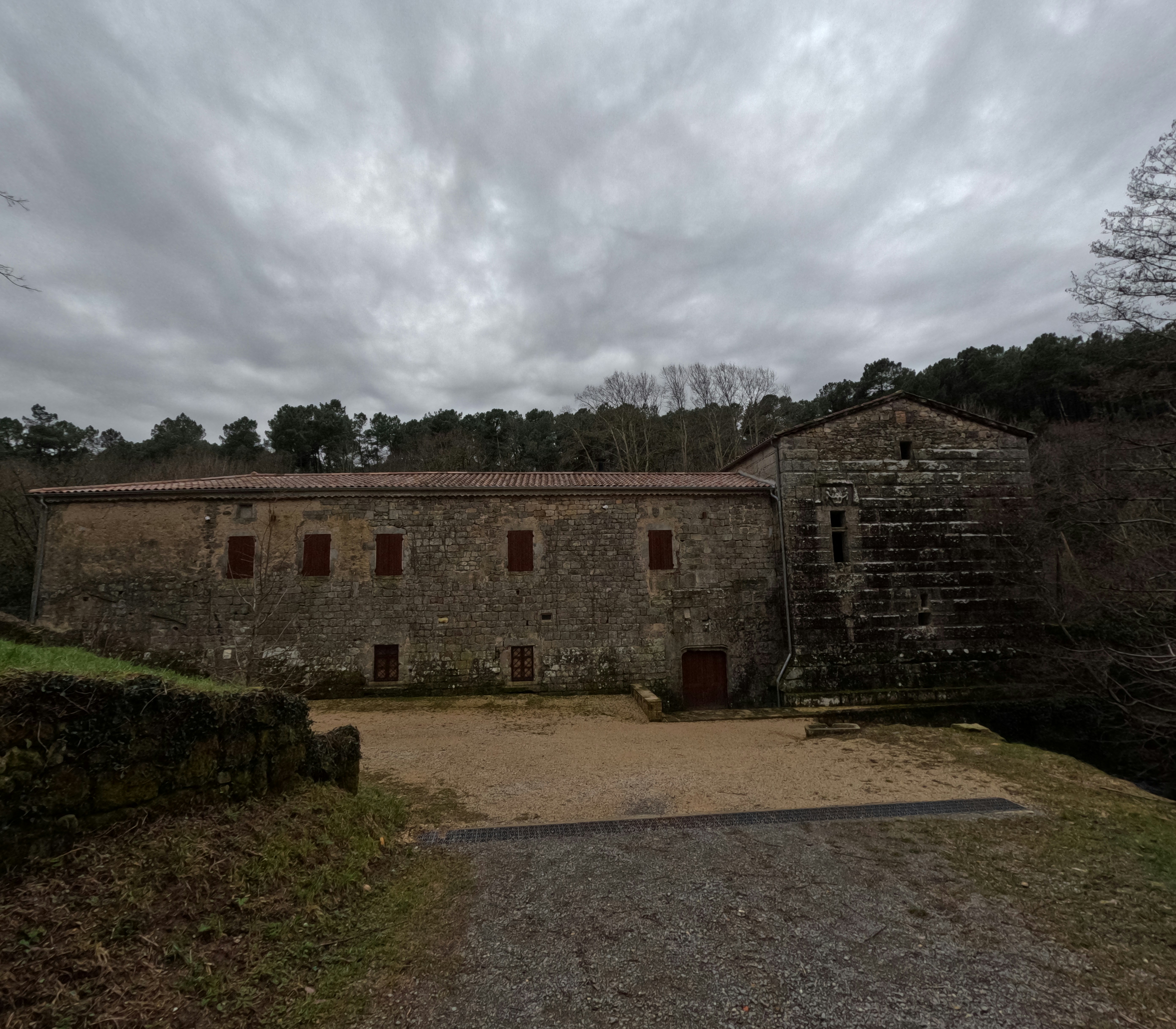Weathered stone millhouse along a gravel forecourt beneath a brooding, cloud-filled sky.