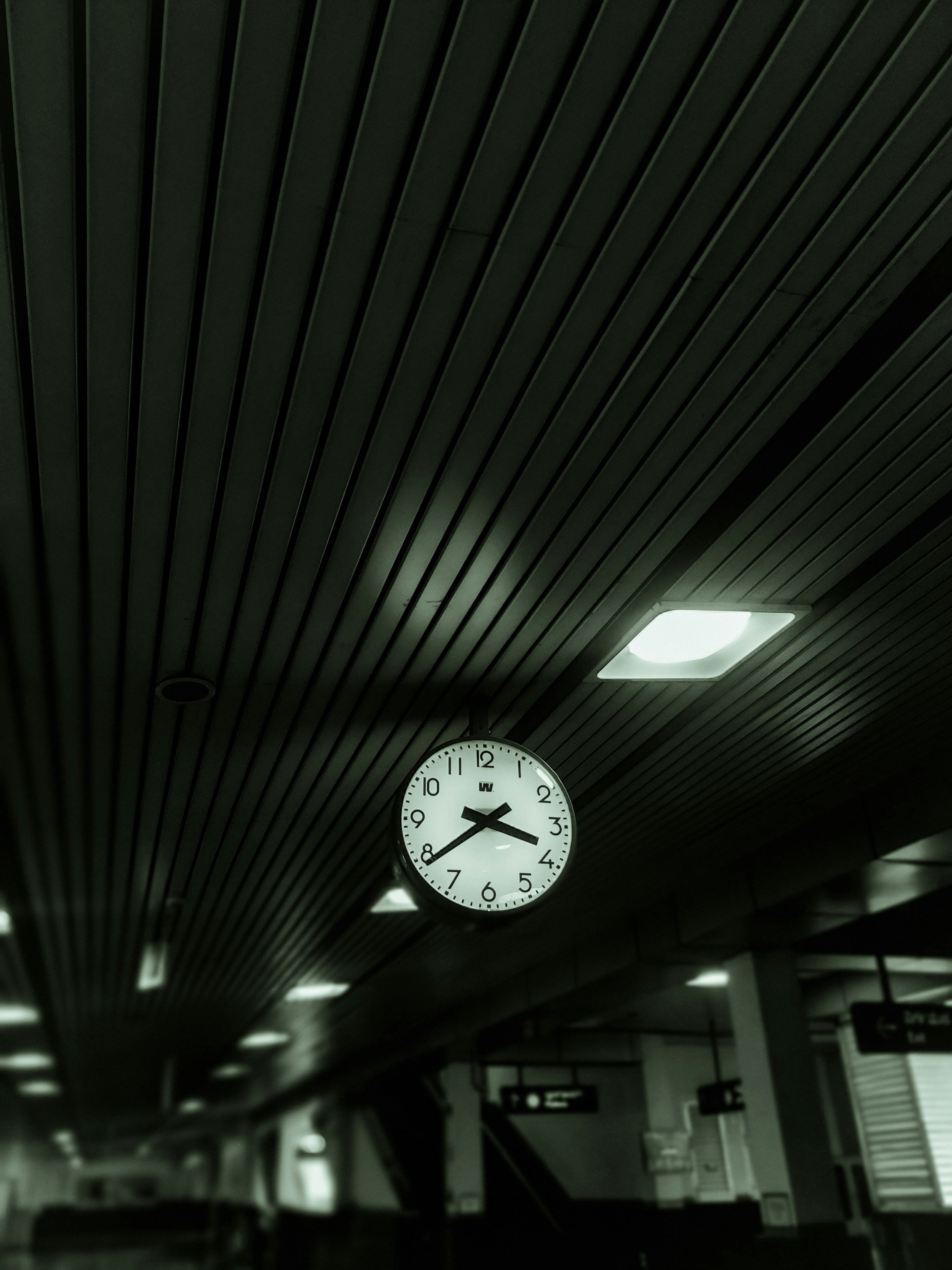 A round clock hangs from a ceiling, capturing the essence of time in a transit space, surrounded by a minimalist architectural design.
