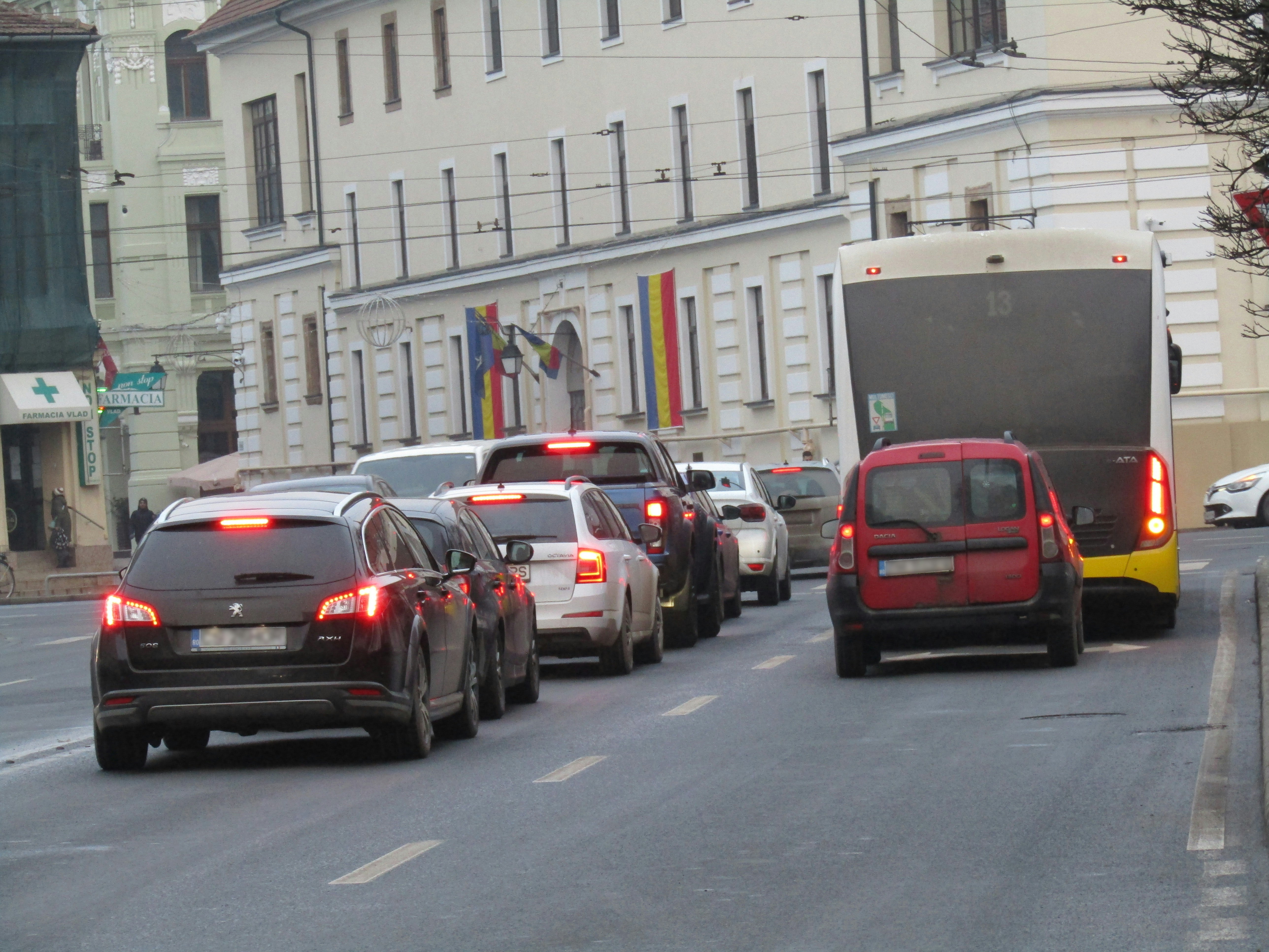 Traffic congestion on a city street lined with historical buildings and colorful flags.