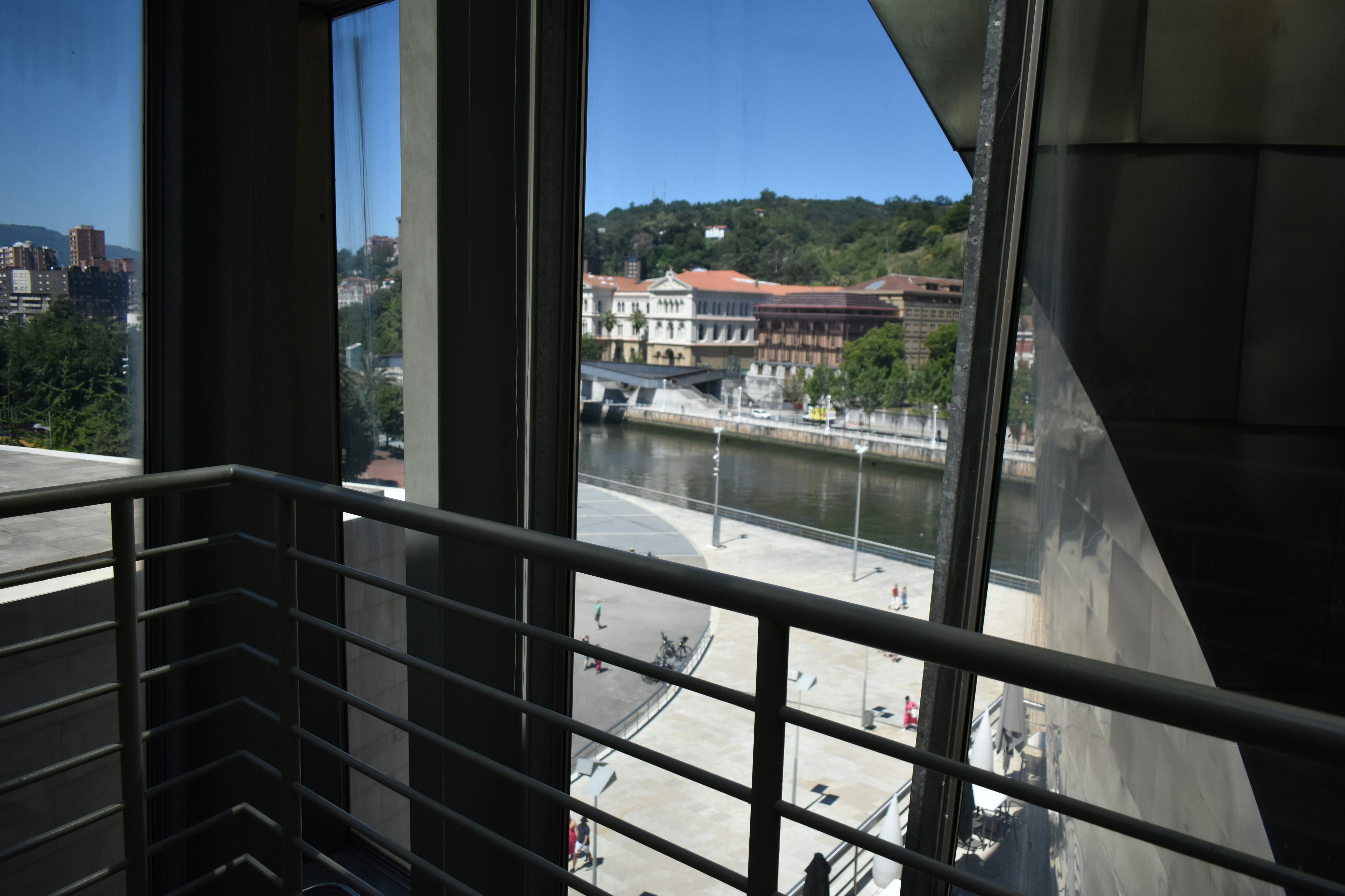 Balcony Frame: Sunlit Riverfront with Bridge and Red-Roofed Buildings