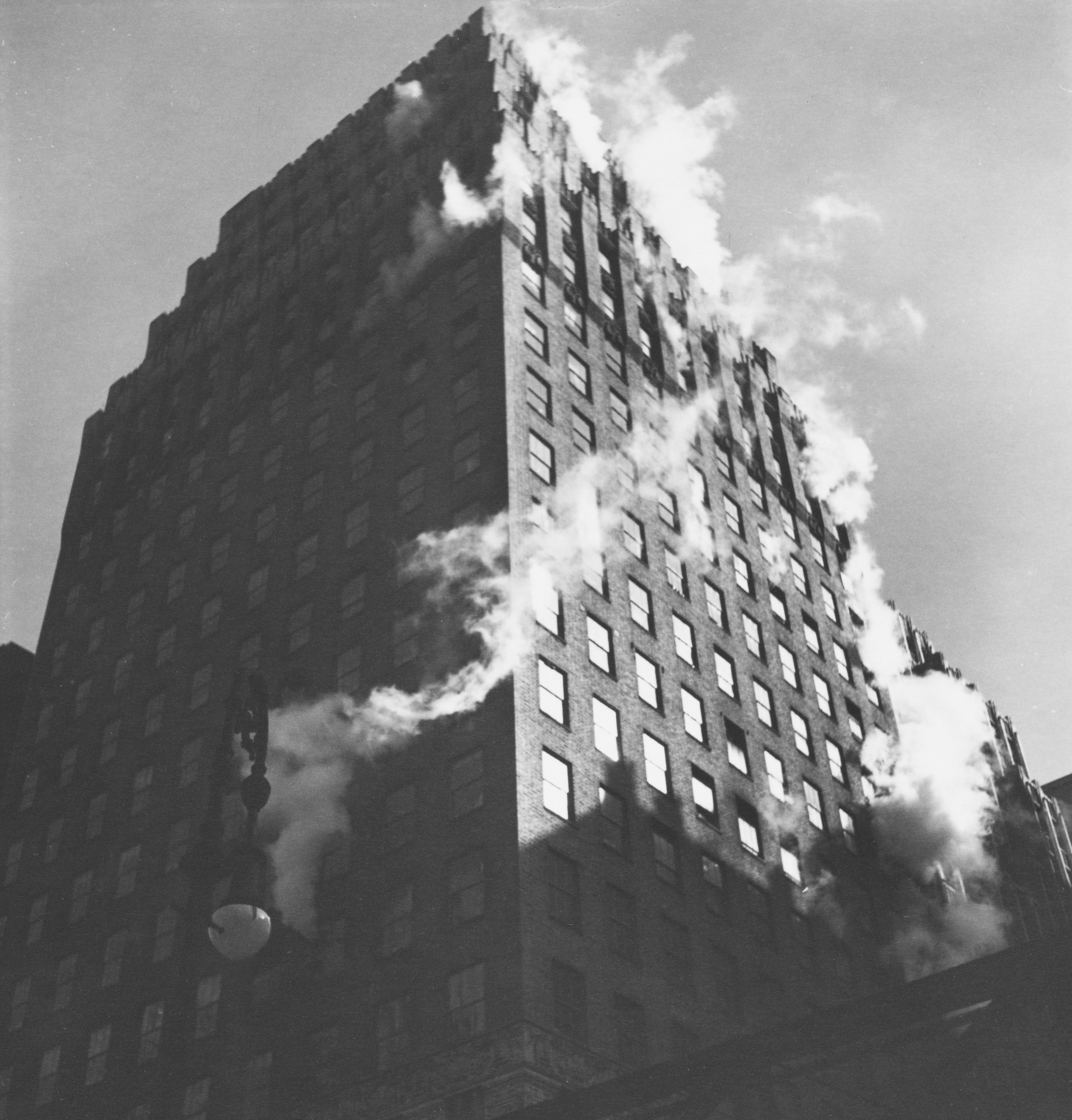 Dark, angular skyscraper vents smoke and steam from multiple peaks, creating dramatic contrast and geometric windows against a pale sky.