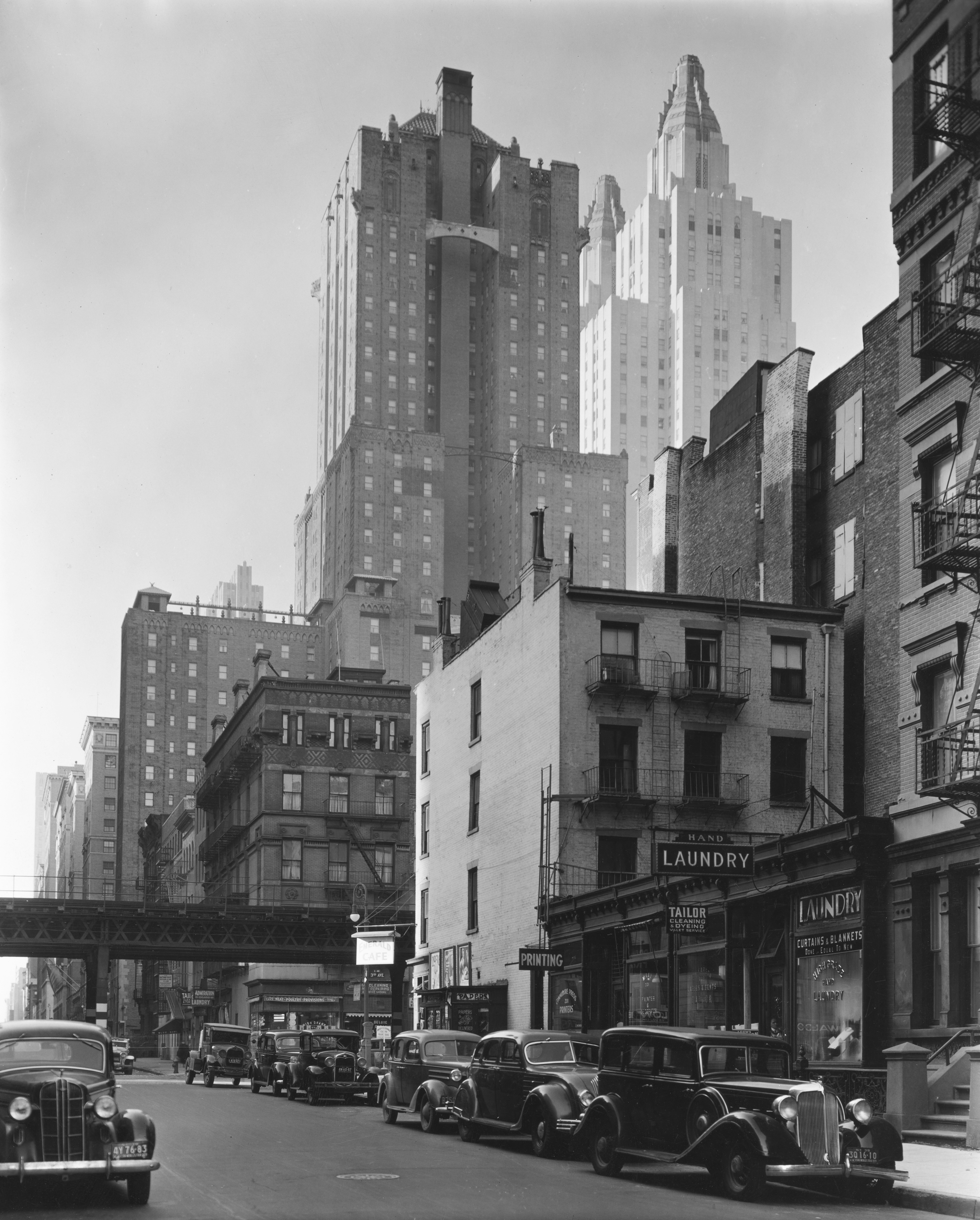 Vintage cars line a bustling street with towering art deco buildings in 1938 New York City.
