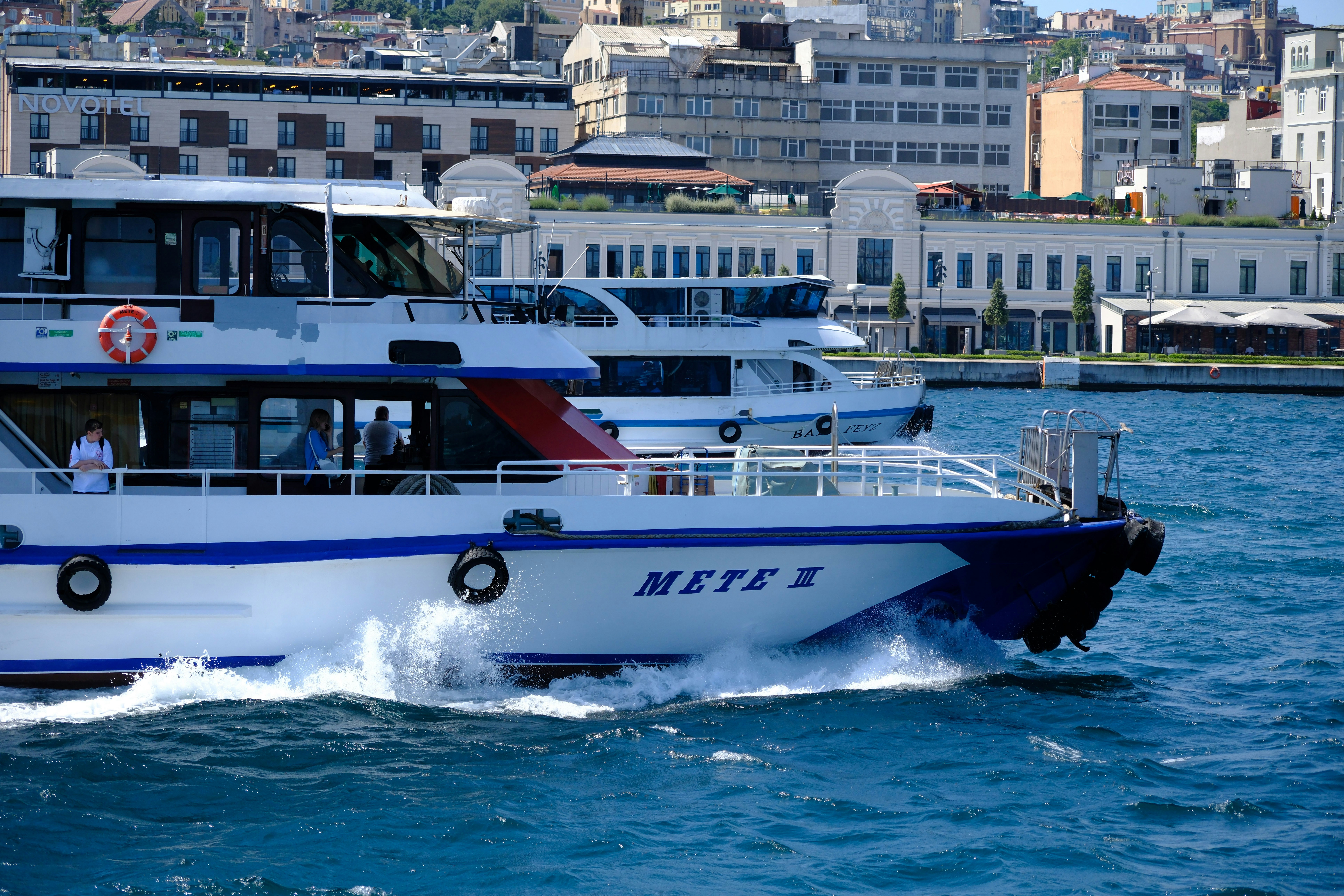 Passenger ferry gliding through vibrant blue waters with urban buildings in the background.