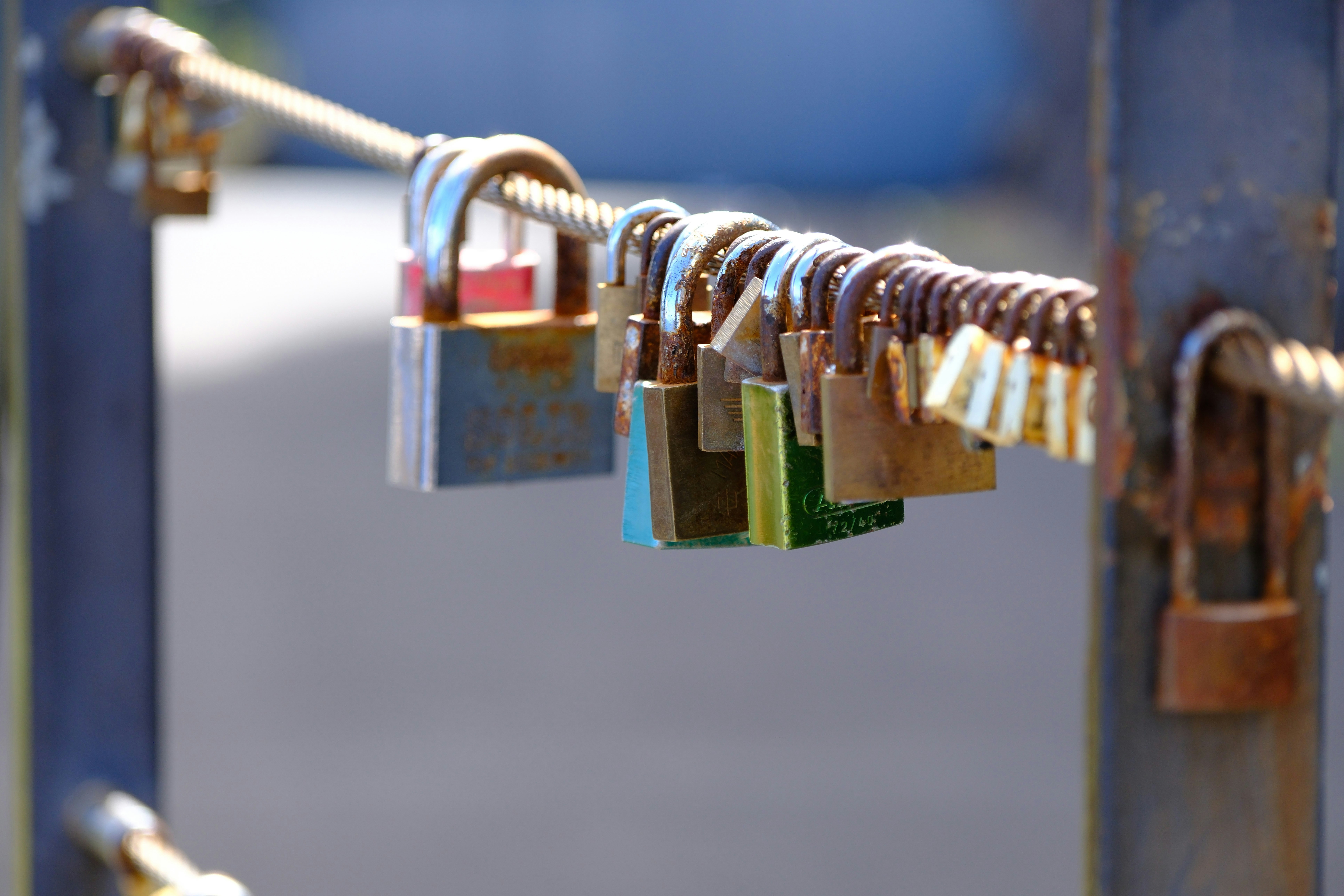 A series of colorful, rusty padlocks hanging on a metal chain, symbolizing memories and security. The focus is on the intricate details of each lock.