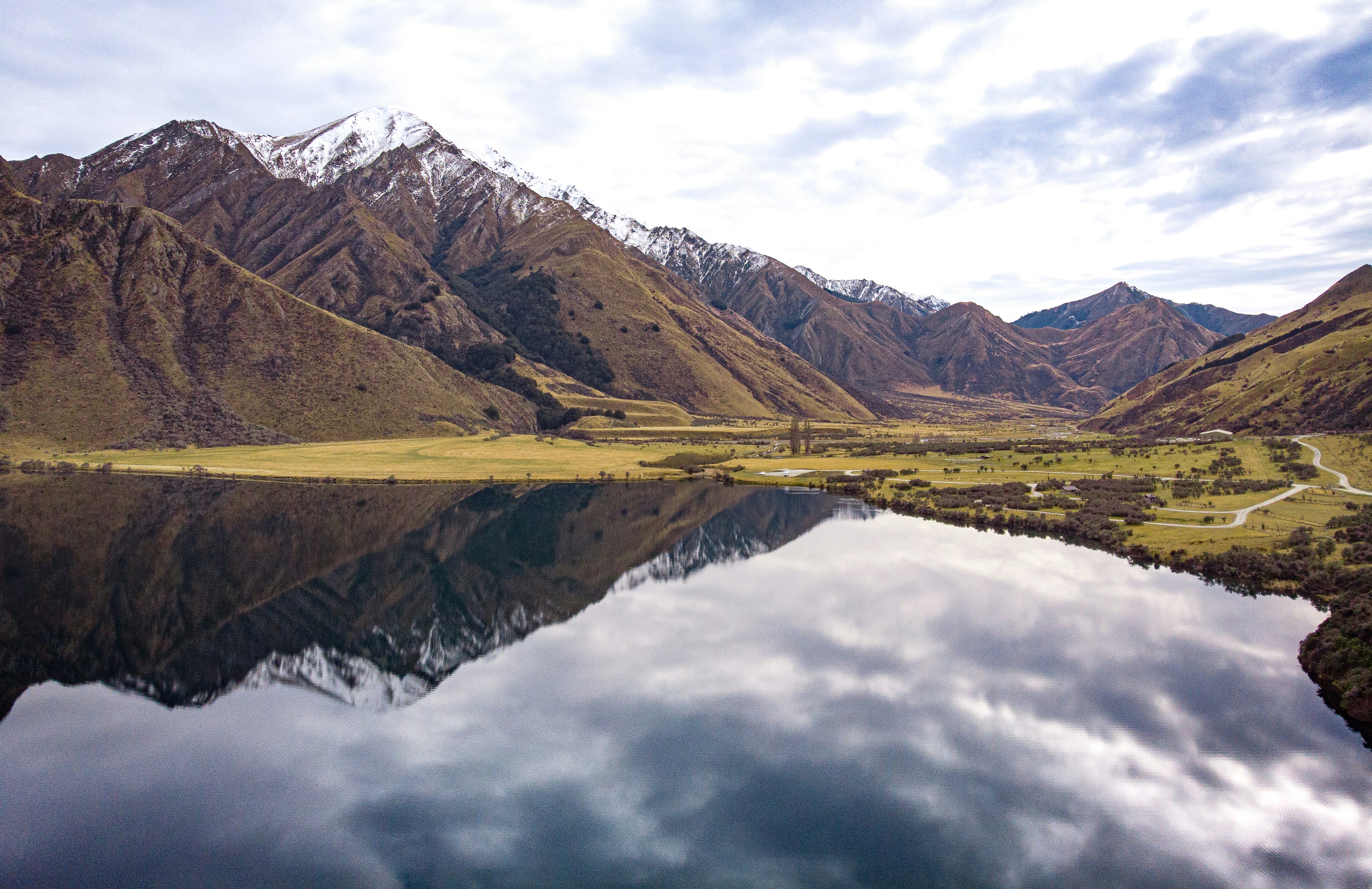 Snow-capped mountains mirrored perfectly in a tranquil lake under a cloudy sky.