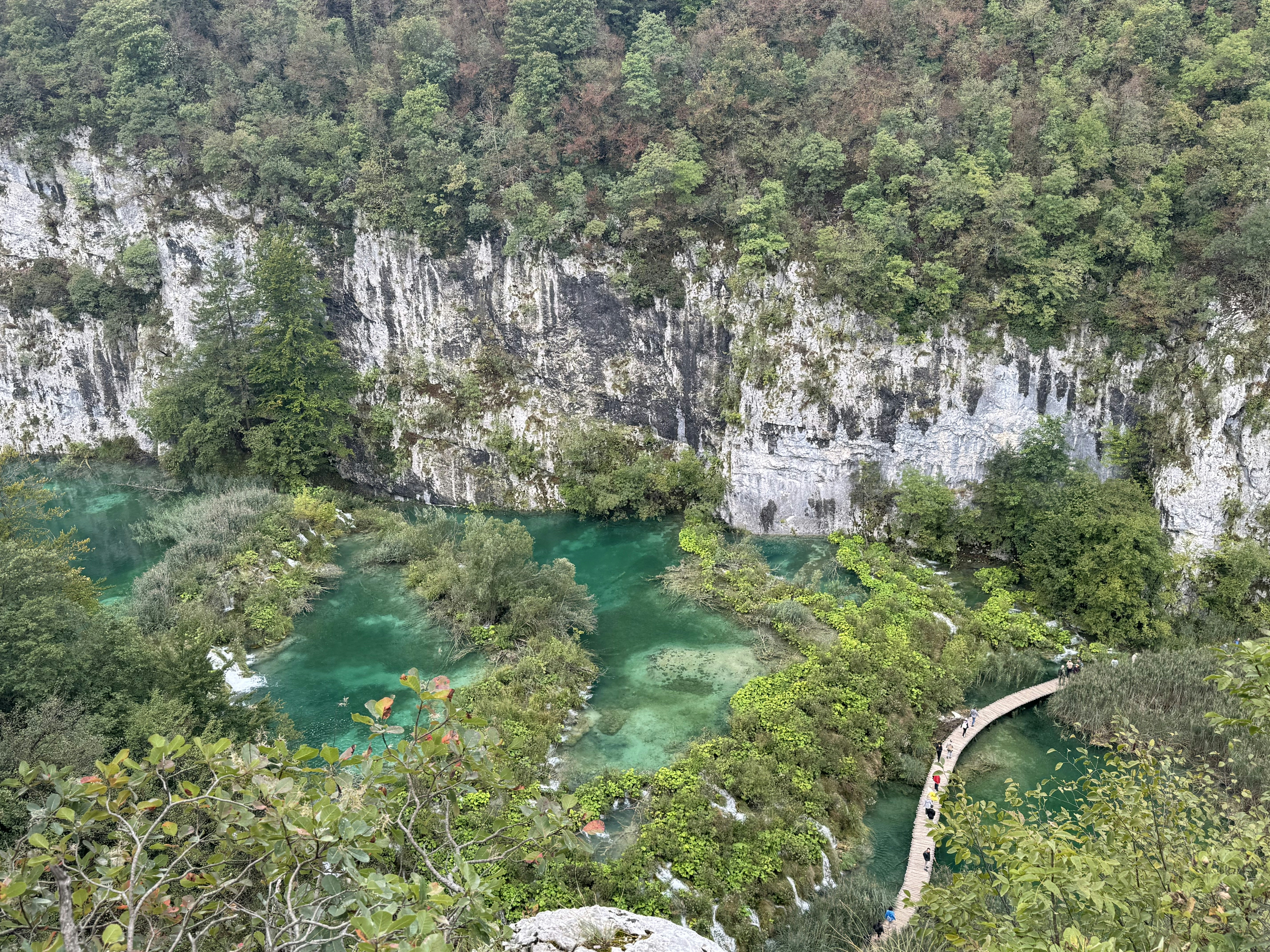 Turquoise river winding through lush greenery and limestone cliffs with a wooden pathway along the bank.