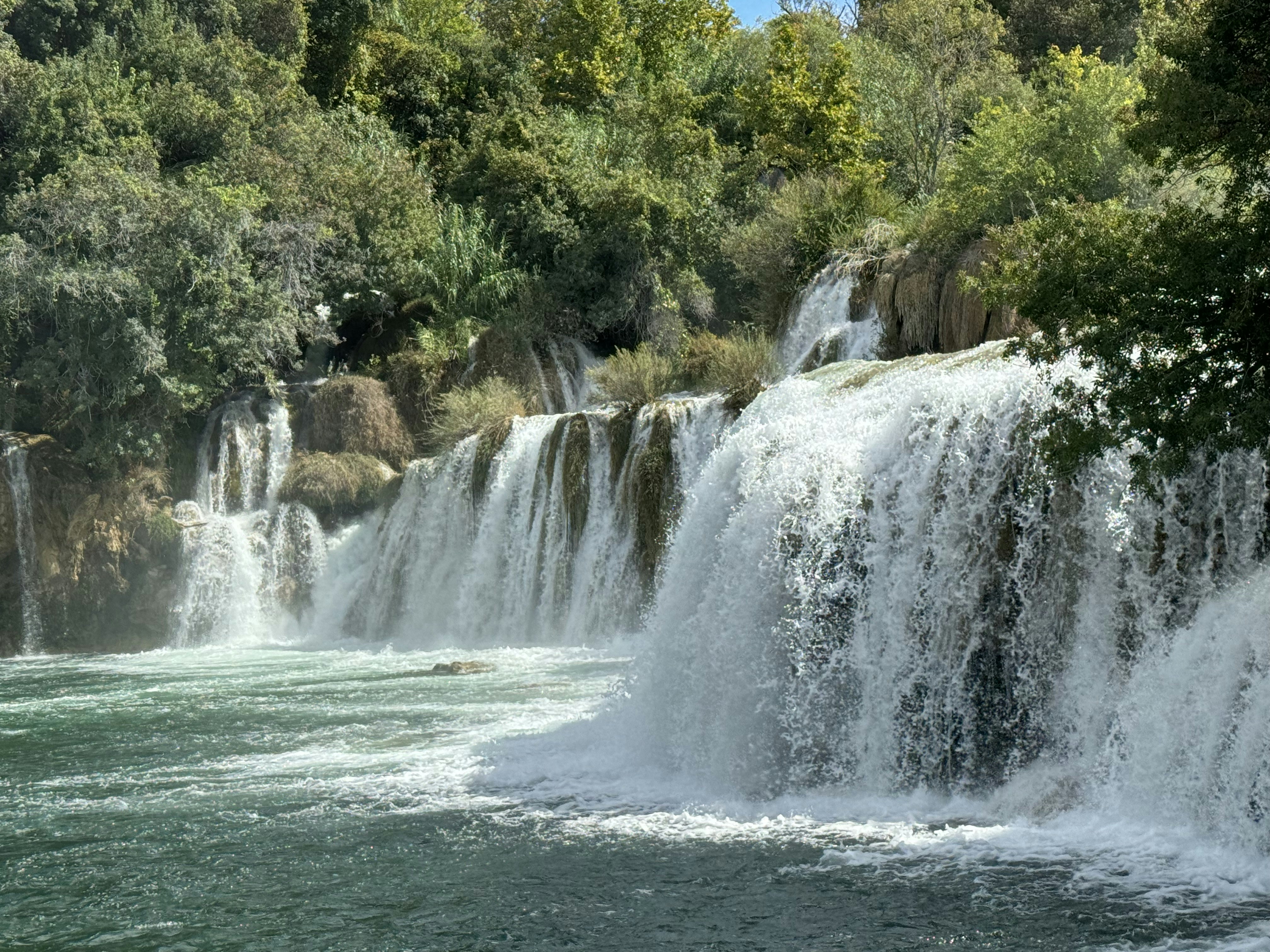 Waterfall cascading over rocky ledges surrounded by lush green foliage under natural light.
