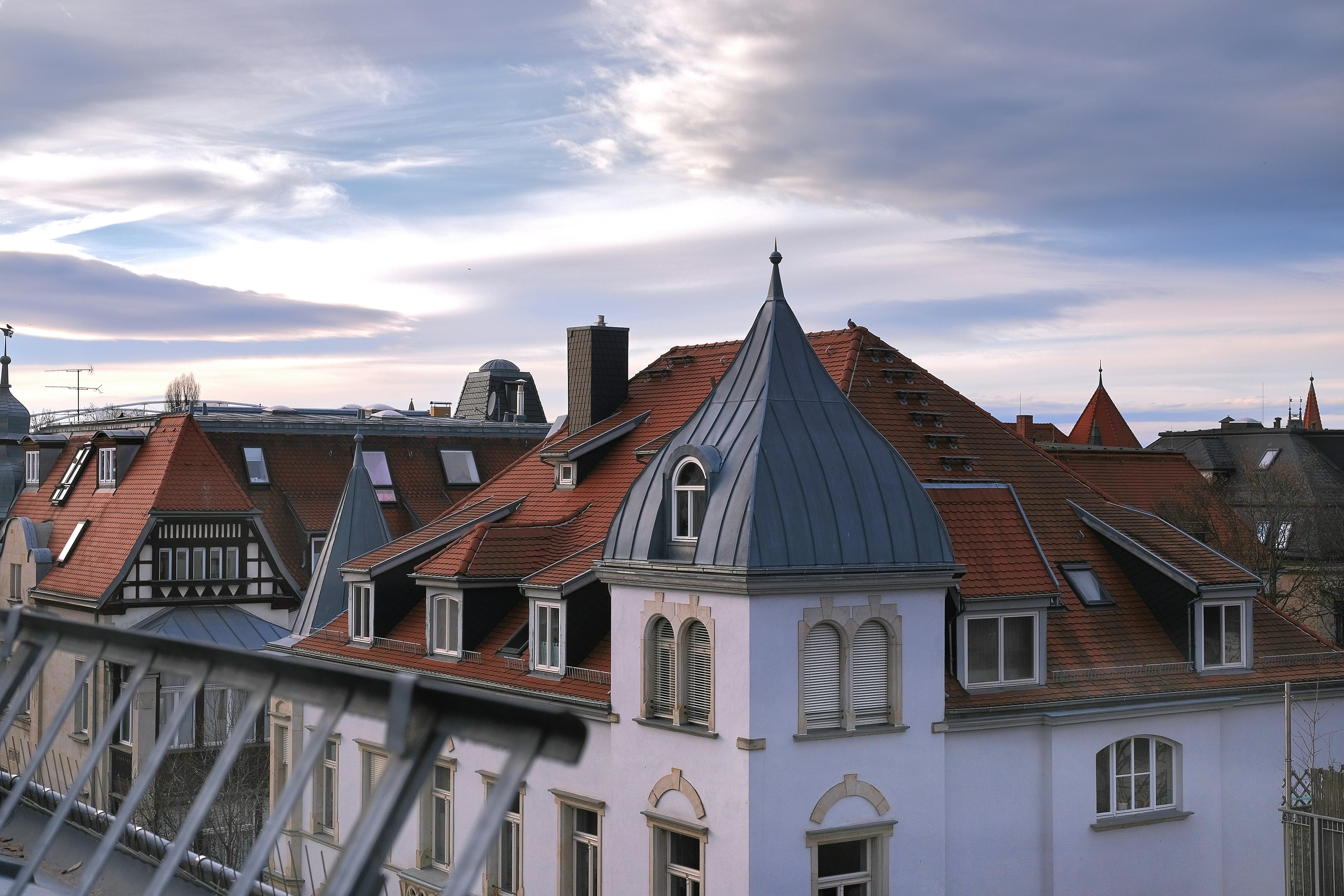 Charming European rooftops with red tiles and a distinctive tower under a dramatic sky.