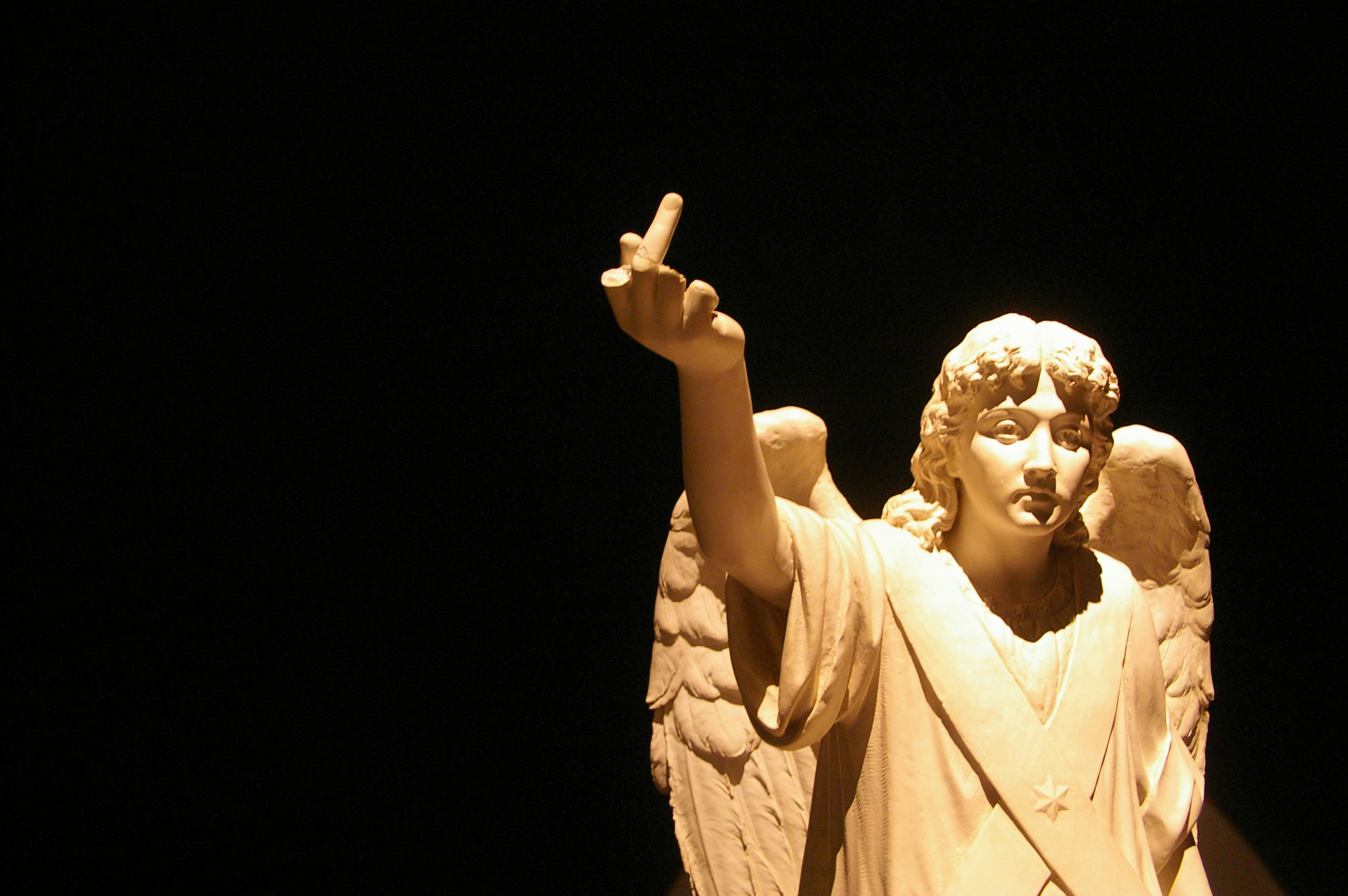 Sculpture of an angel with outstretched arm, dramatically lit against a stark black background.
