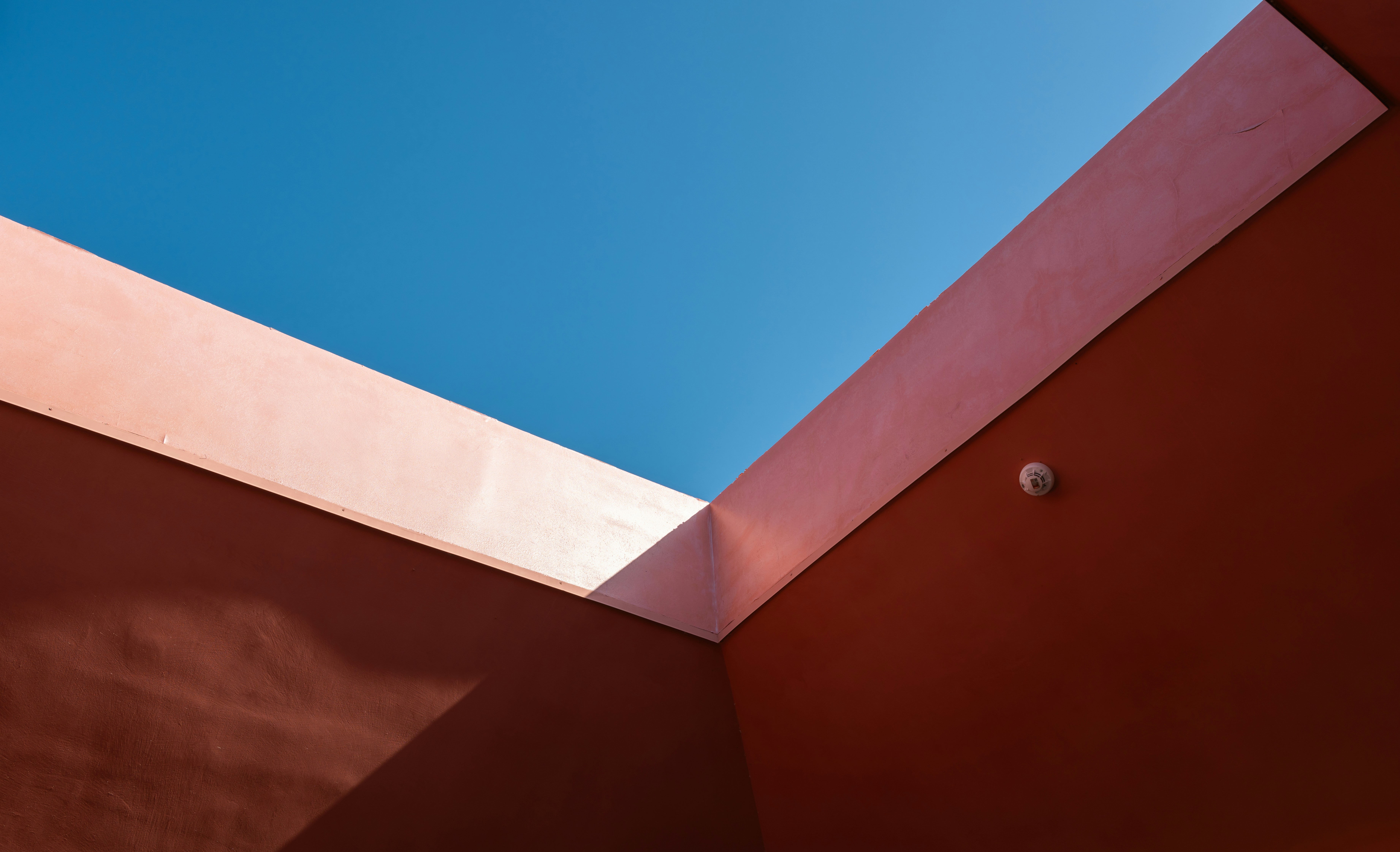 Minimalist architecture with sharp terracotta lines set against a vibrant blue sky. Light and shadow interplay adds depth and visual interest.