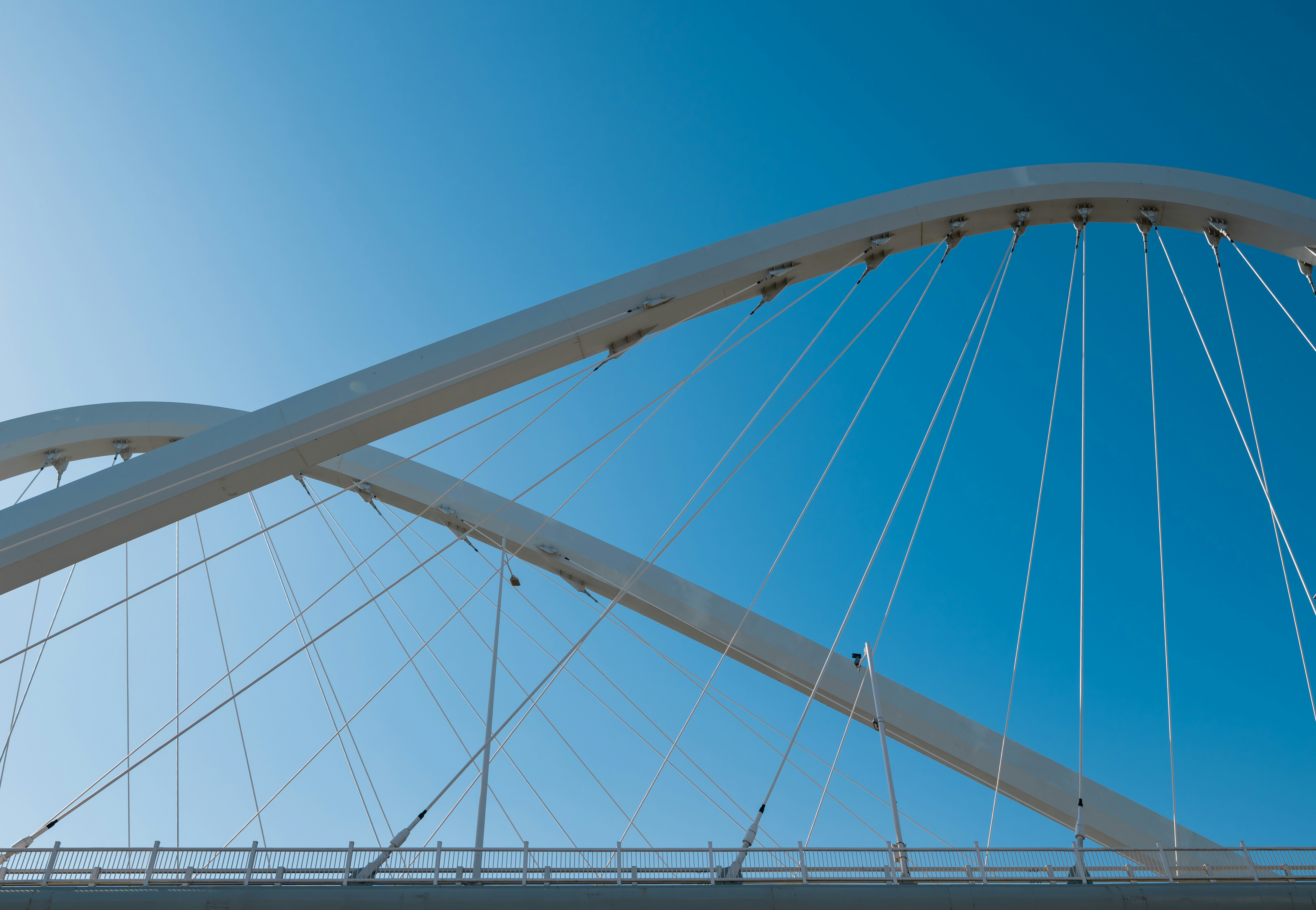White arched bridge with cables set against a vibrant blue sky, highlighting geometric lines and symmetry.