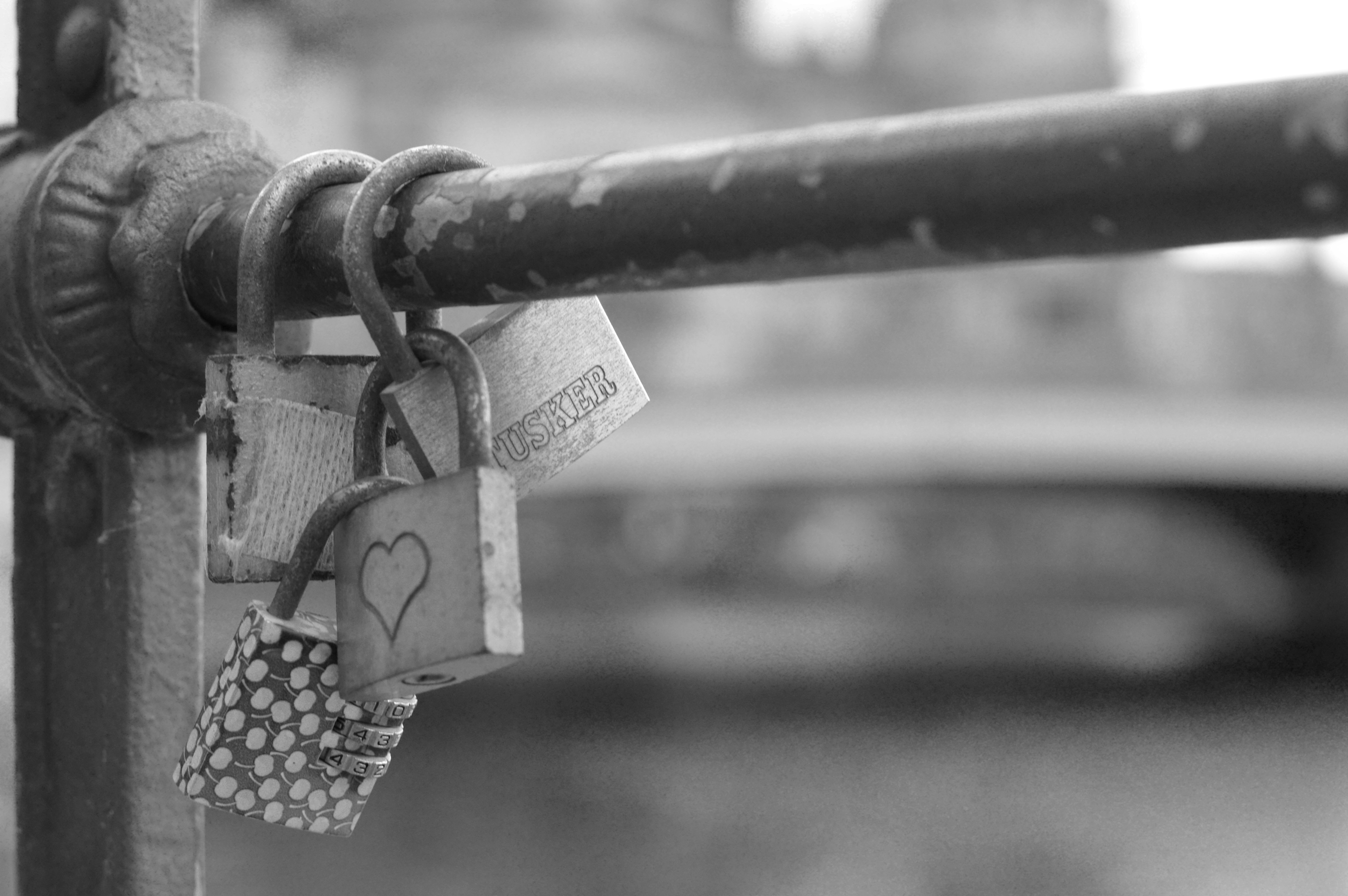 Love locks hanging on a rusted metal railing, with an engraved heart symbolizing enduring affection. Monochrome tones highlight the contrast between the industrial texture and sentimental meaning.