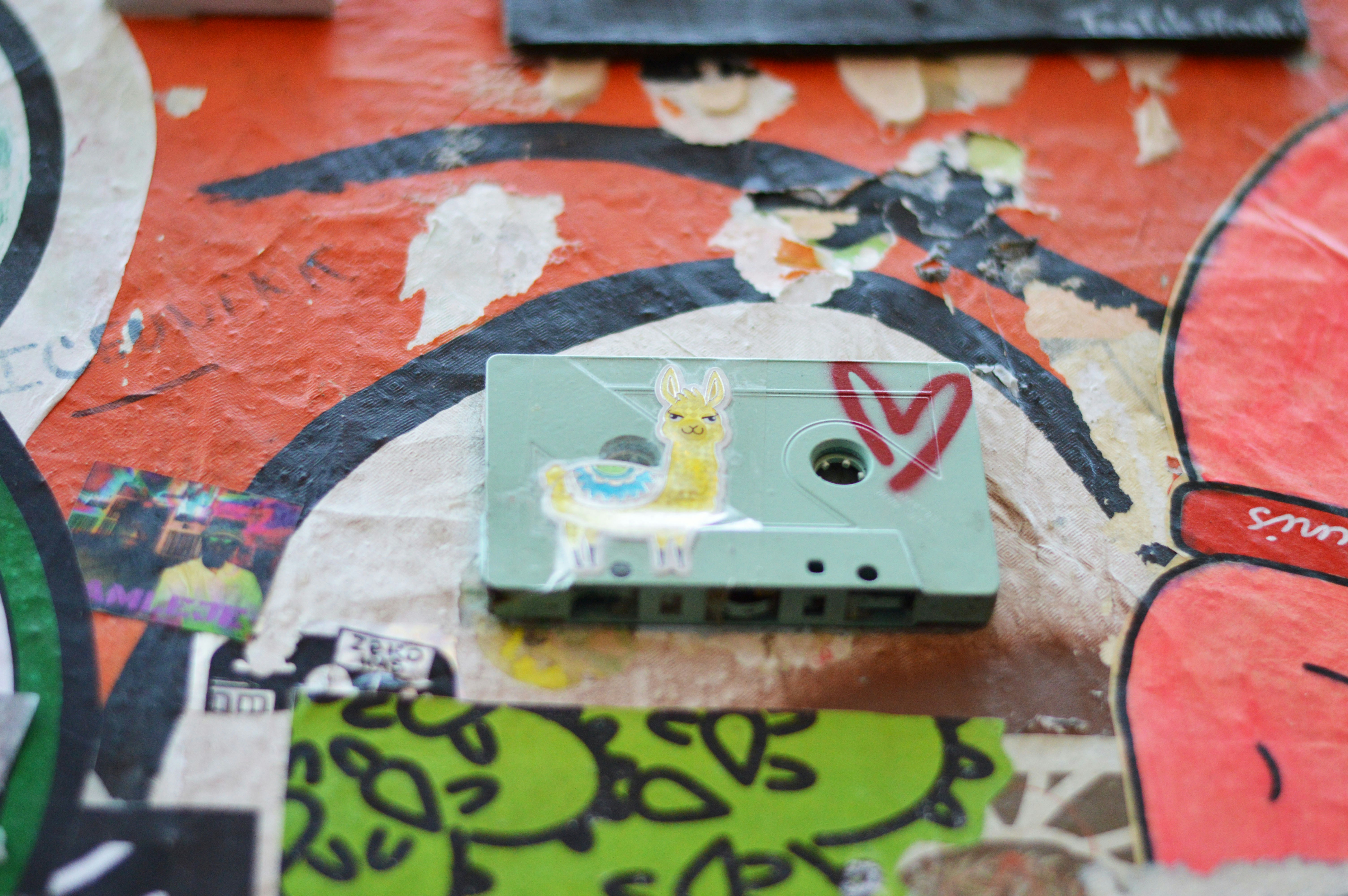 Pastel green cassette with llama sticker and red heart on vibrant collage background.