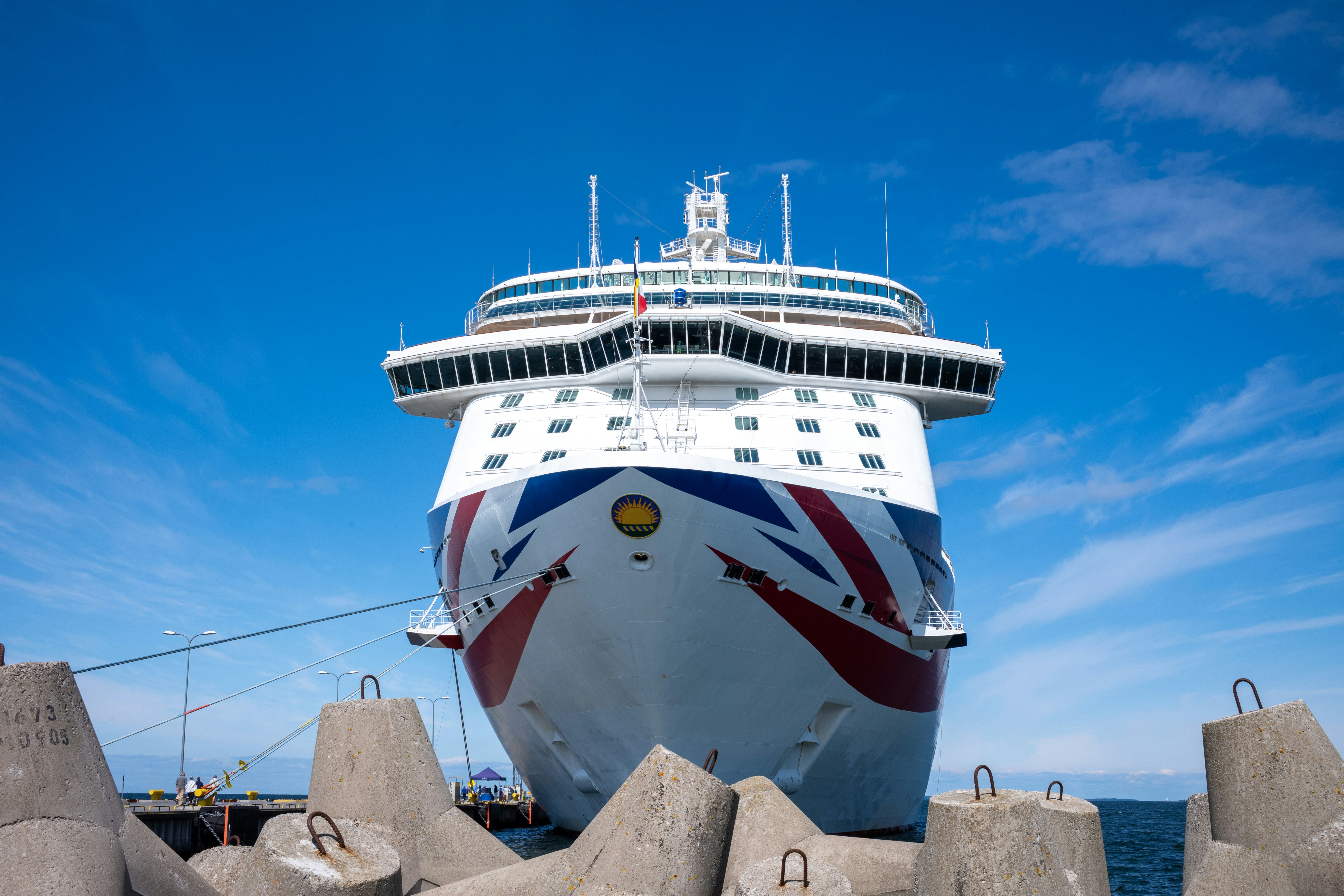 Cruise ship docked against a clear blue sky with geometric concrete structures in the foreground.
