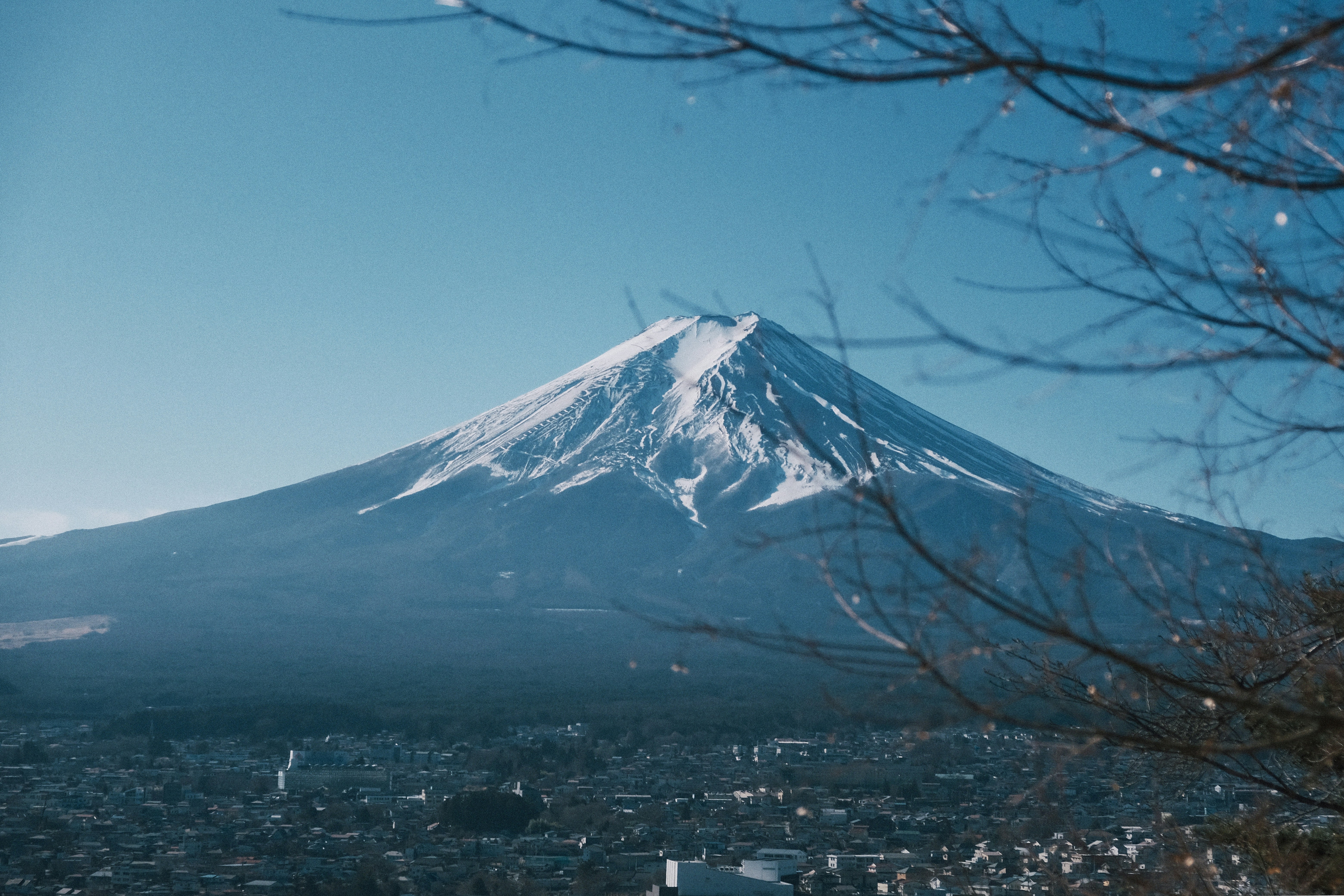 Snow-capped Mount Fuji under a clear blue sky with cityscape in the foreground.