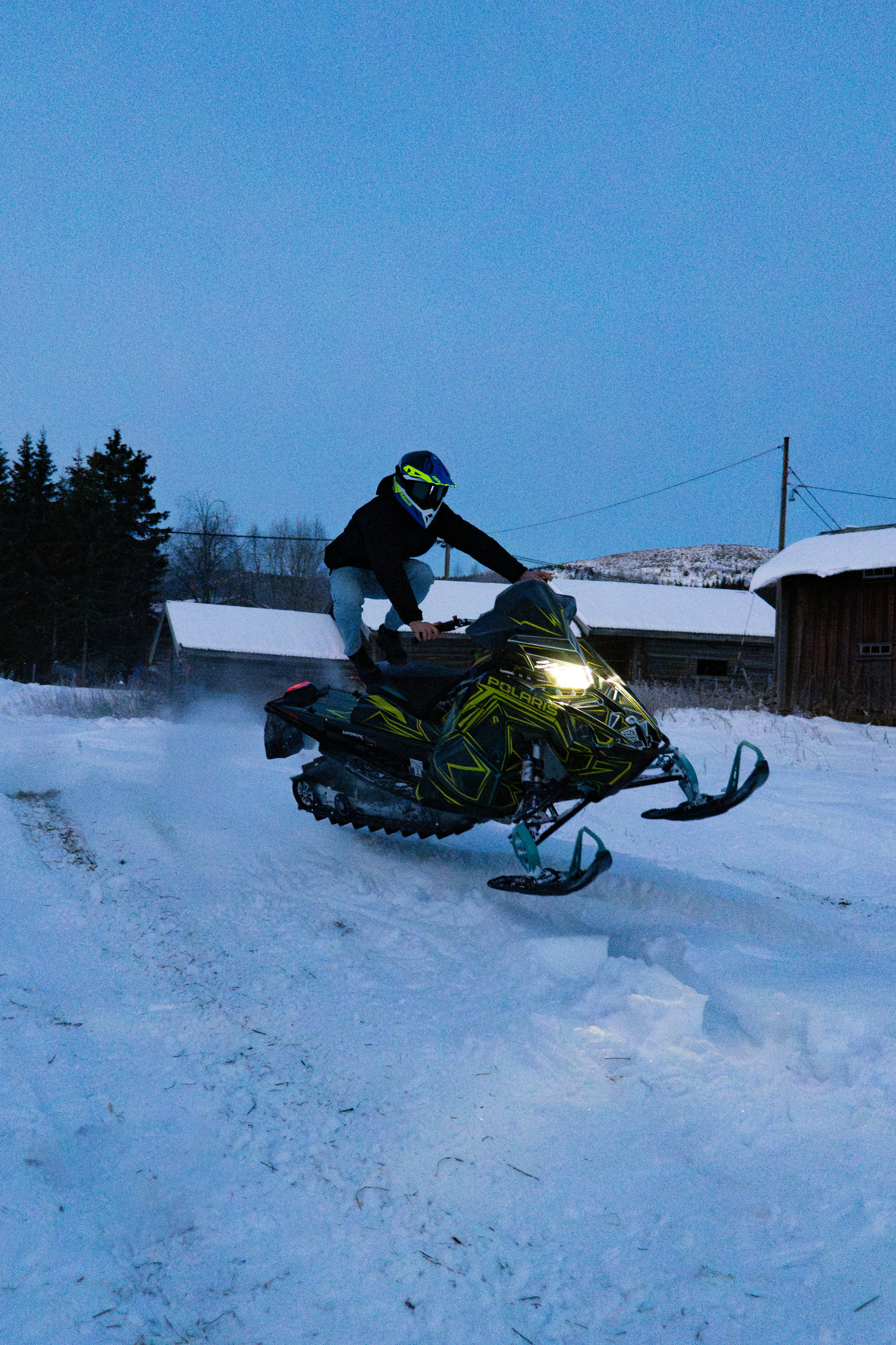 Neon Trails in Blue Hour: Snowmobile Leap over a Quiet Farm