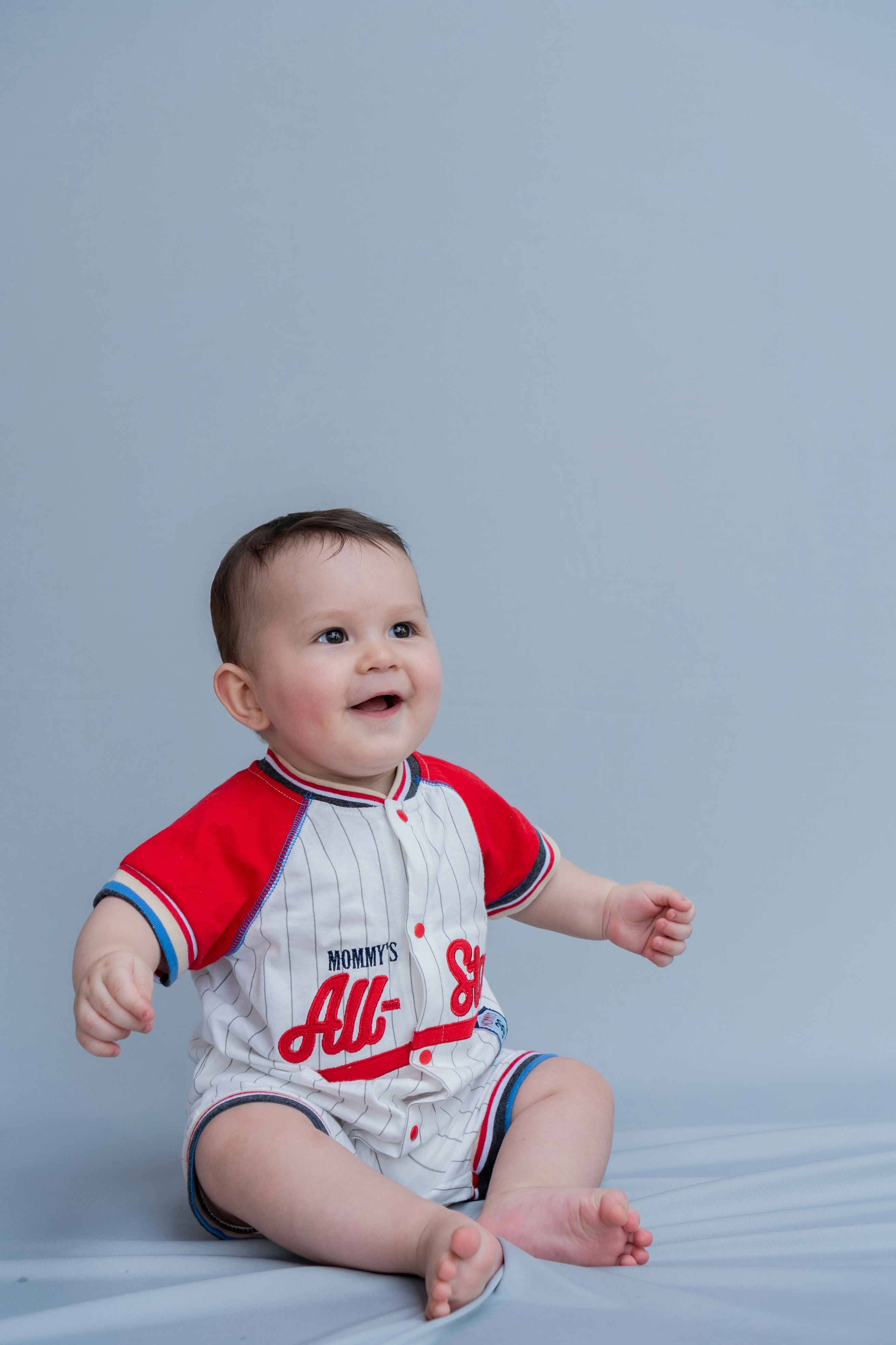 A baby sitting on the ground wearing a baseball uniform photo – Free ...