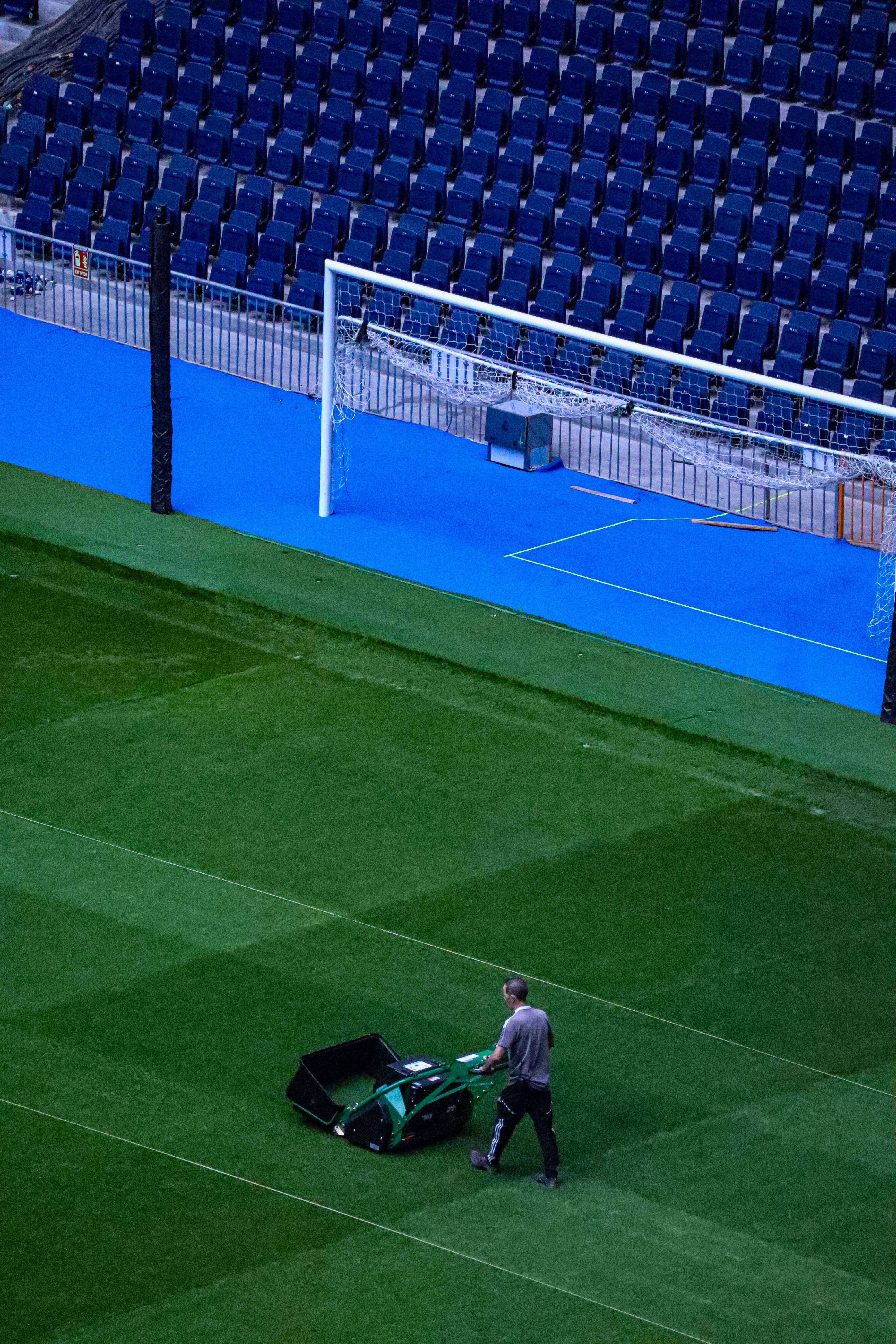 The Quiet Mow: A Groundskeeper Tames the Pitch Beneath Empty Blue Seats
