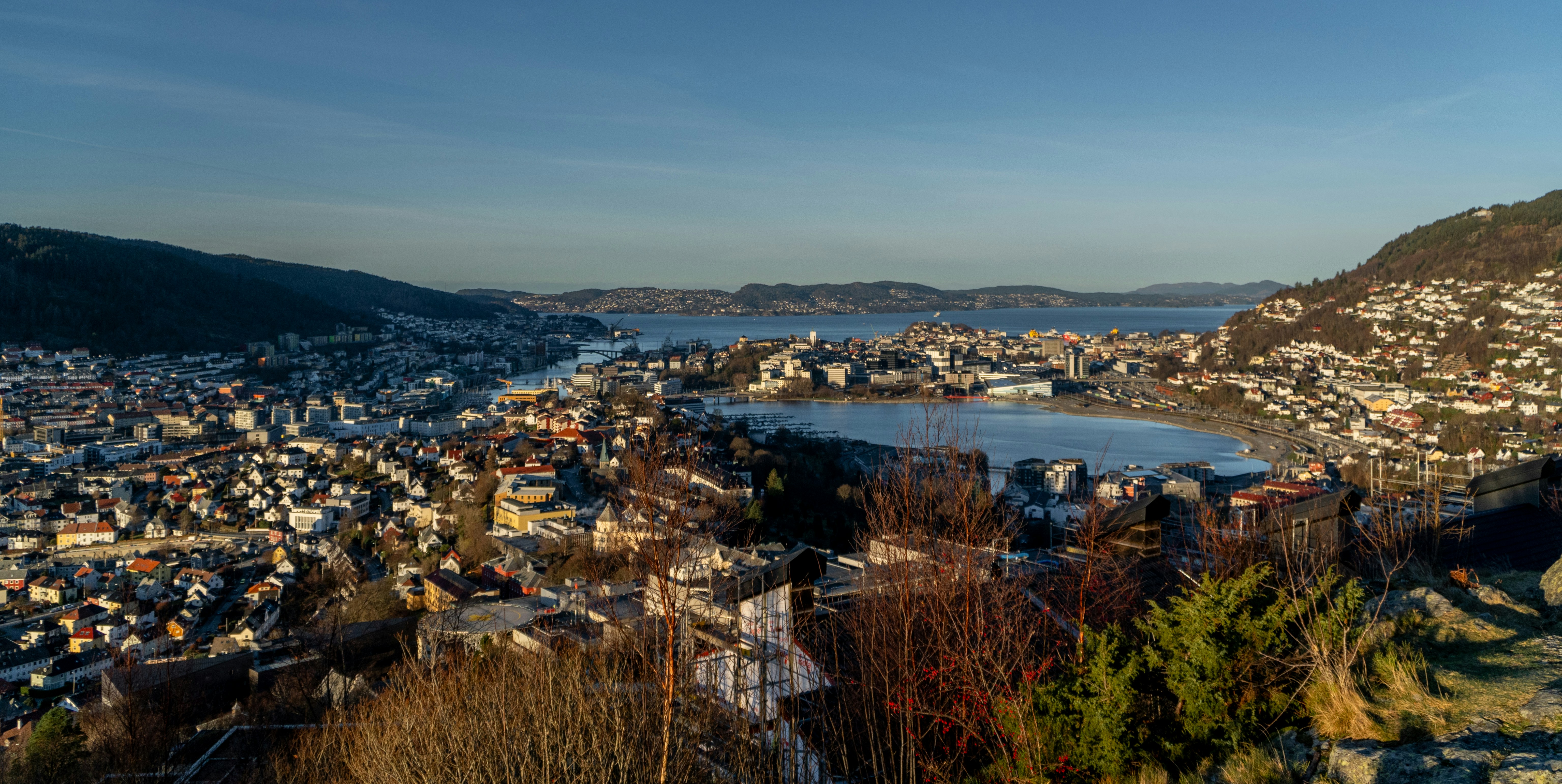 Panoramic view of Bergen, Norway, with sunlight illuminating the city and harbor under a clear sky.