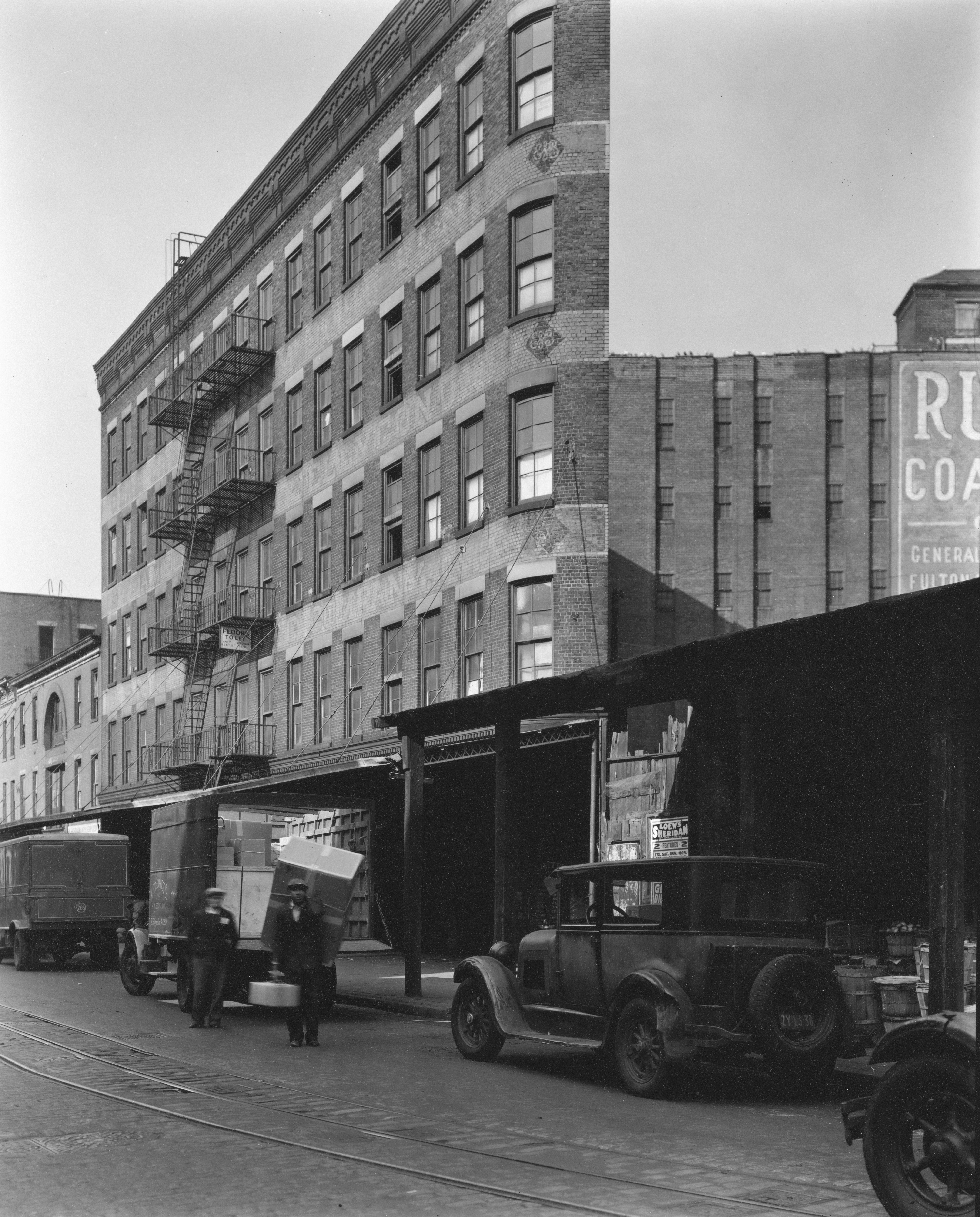 Historic street scene with vintage vehicles and workers outside a brick building on Gansevoort Street.
