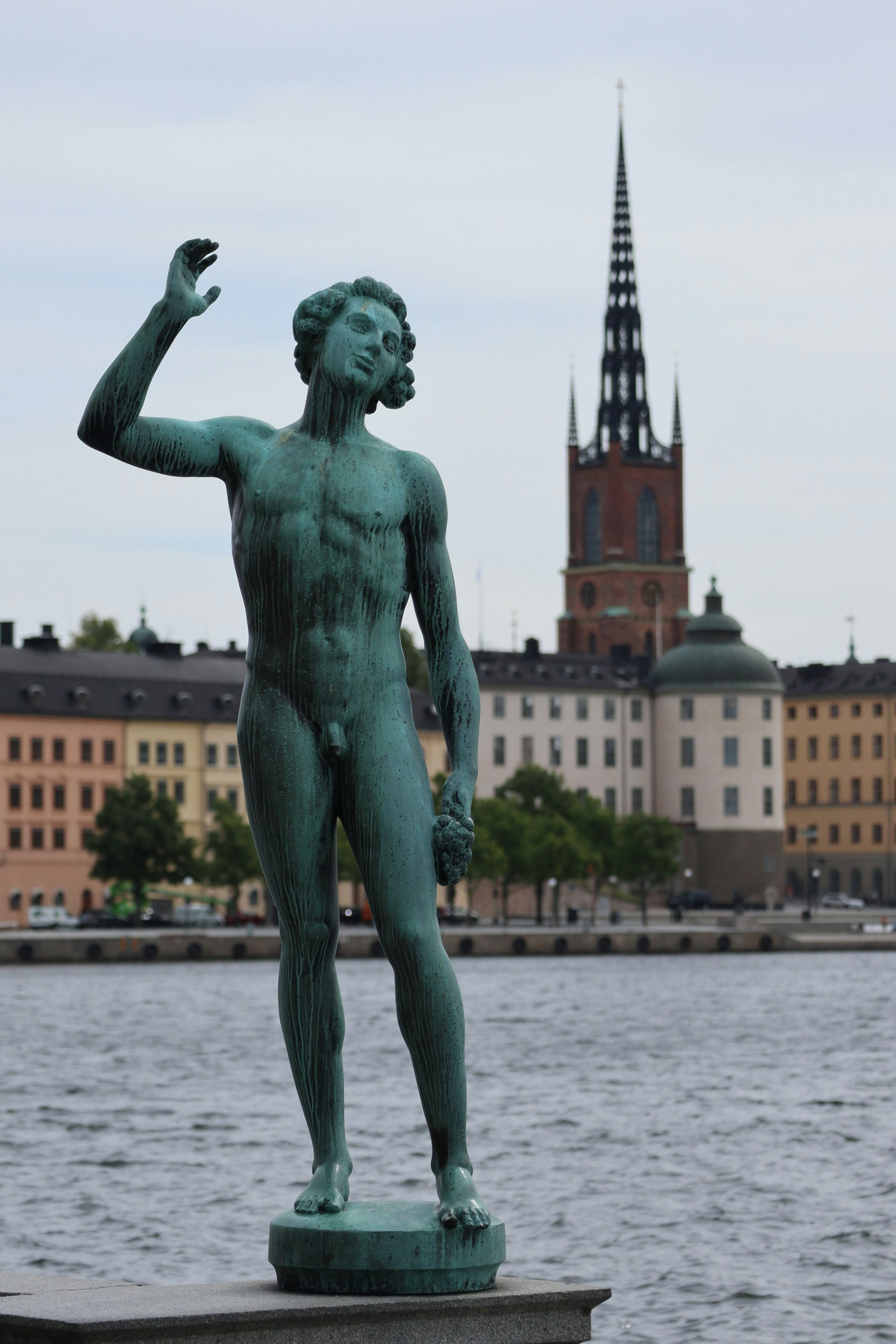 Verdigris Sentinel by the Waterfront: Bronze Nude Framed by a Historic City Spire