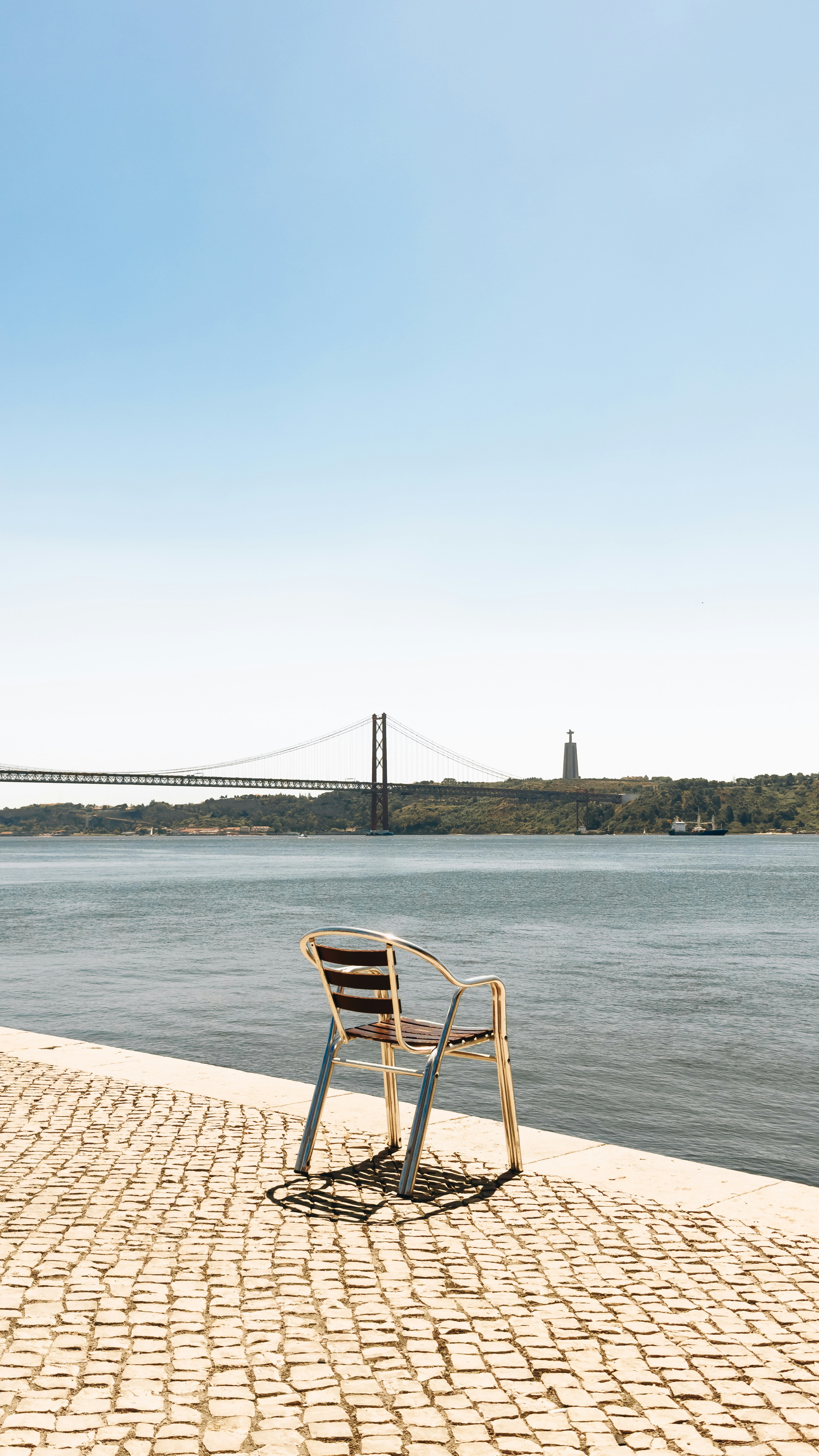 Solitary Chair by the River: Echoes of a Bridge and Horizon