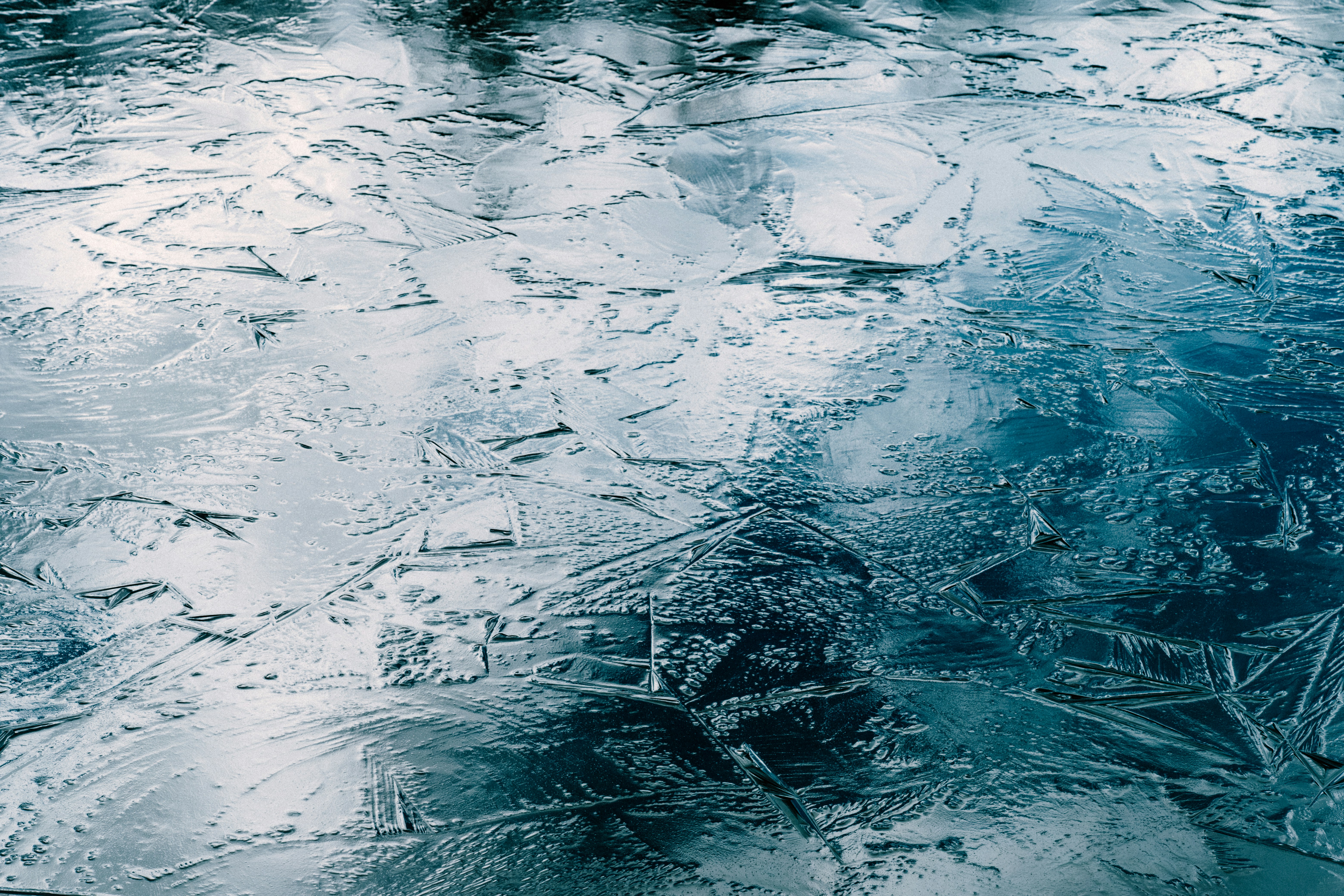 Complex ice formations cover a frozen lake with a subtle blue tint in the French Alps.