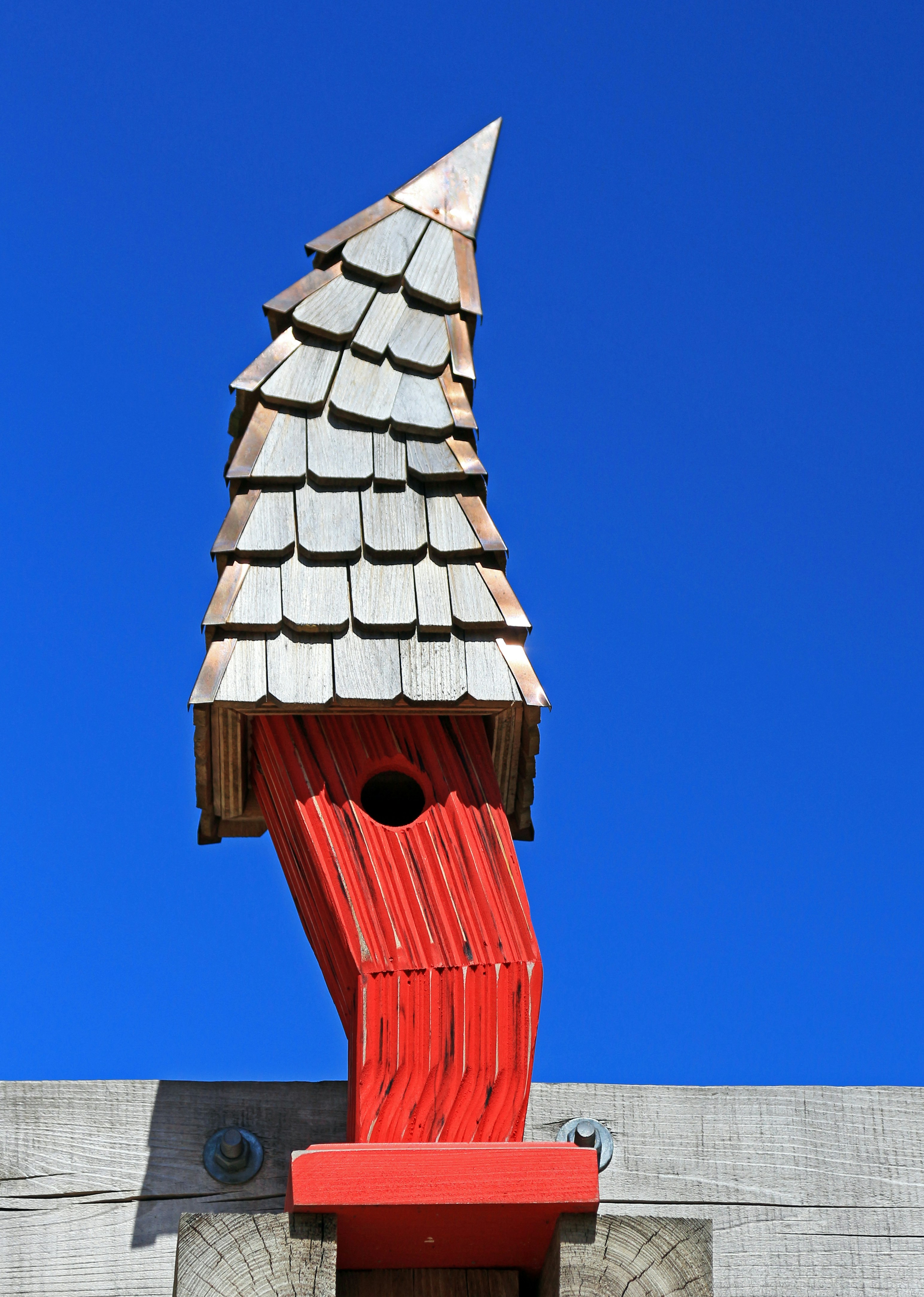 A red birdhouse with a white roof and a blue sky in the background ...