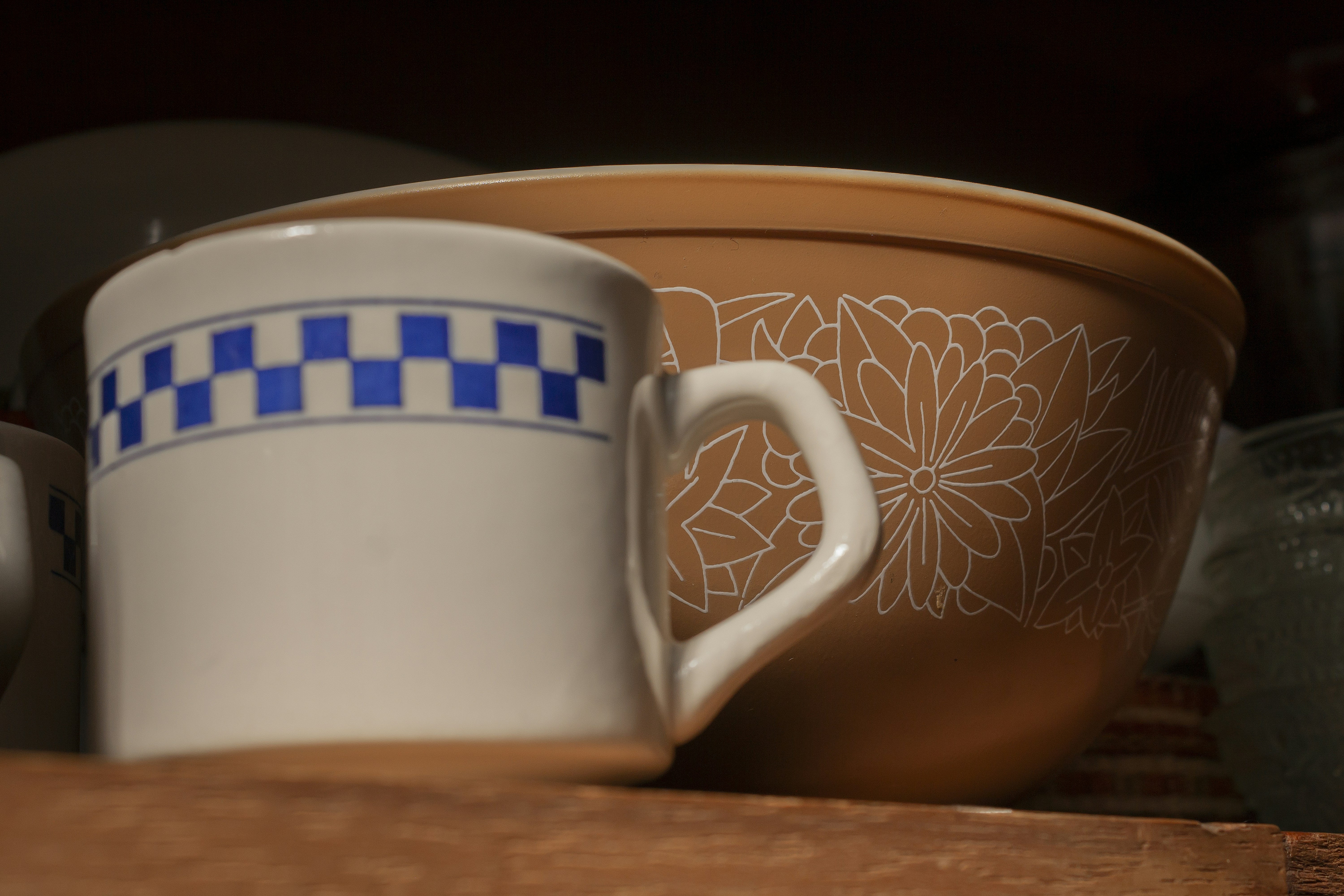 Vintage ceramic mug with blue checkered pattern beside a large bowl with intricate floral design in warm tones.