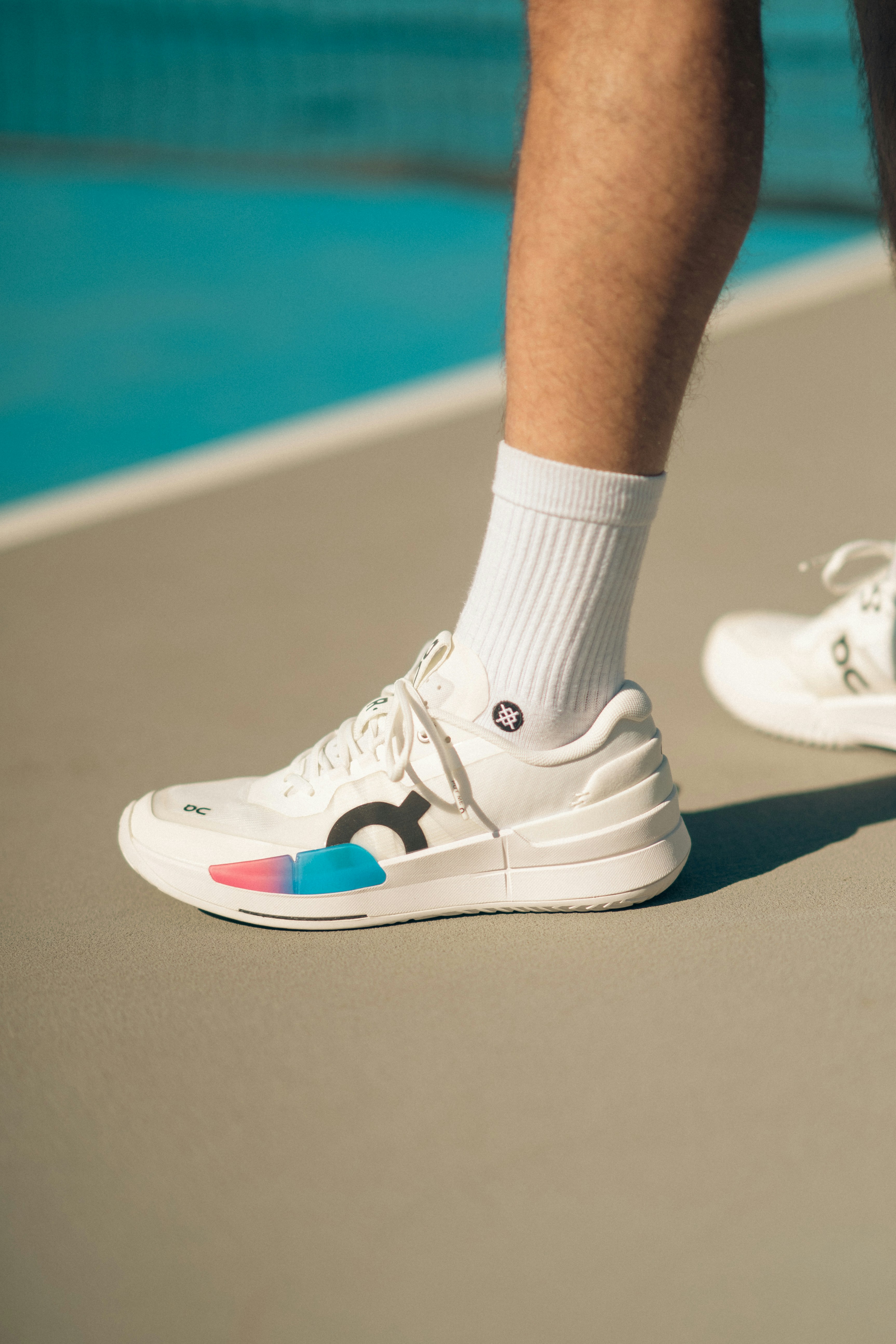 White athletic sneakers with colored badge and heel accents on a sunlit track surface