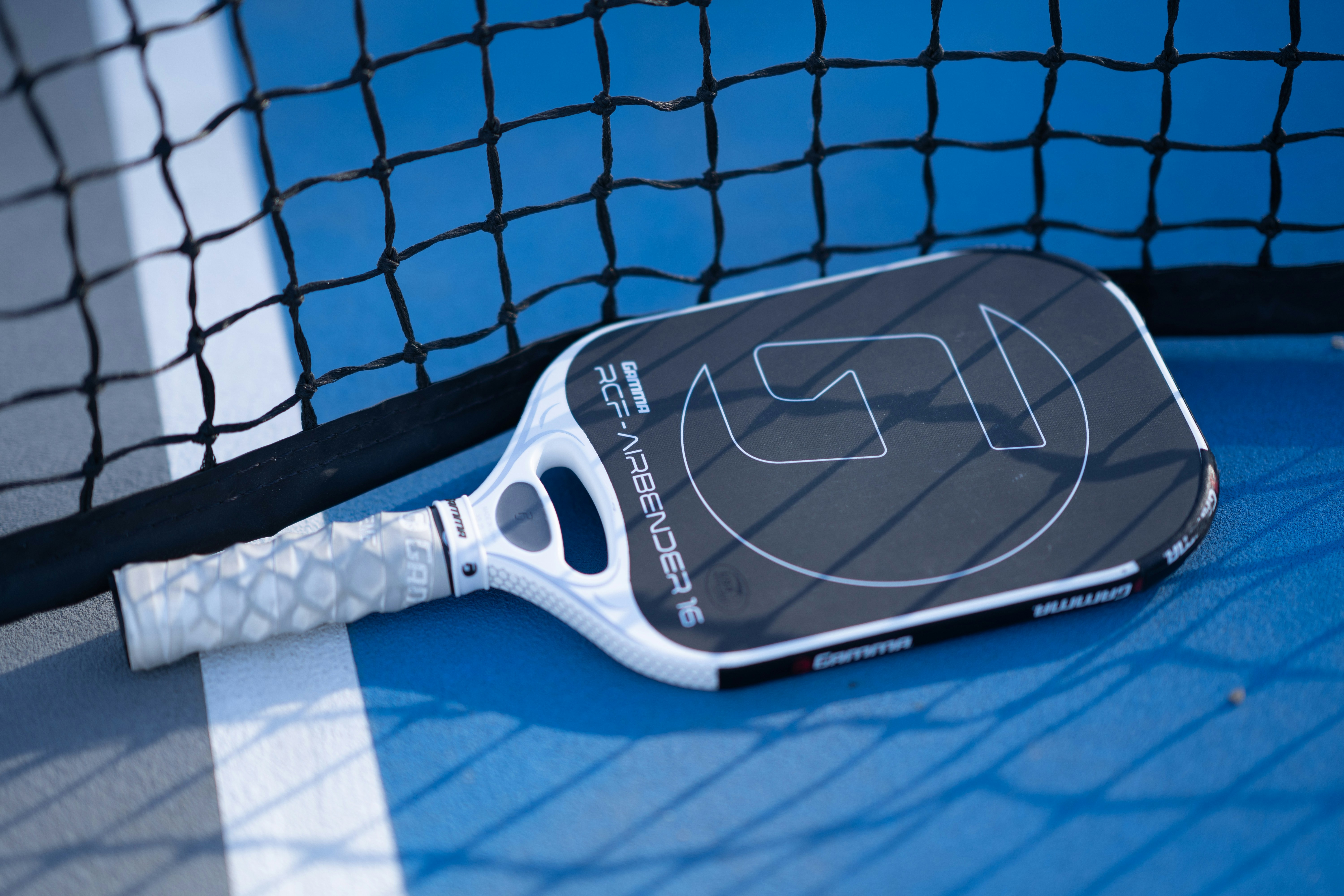 Blue Silence: A Padel Paddle Resting by the Net on a Sunlit Court