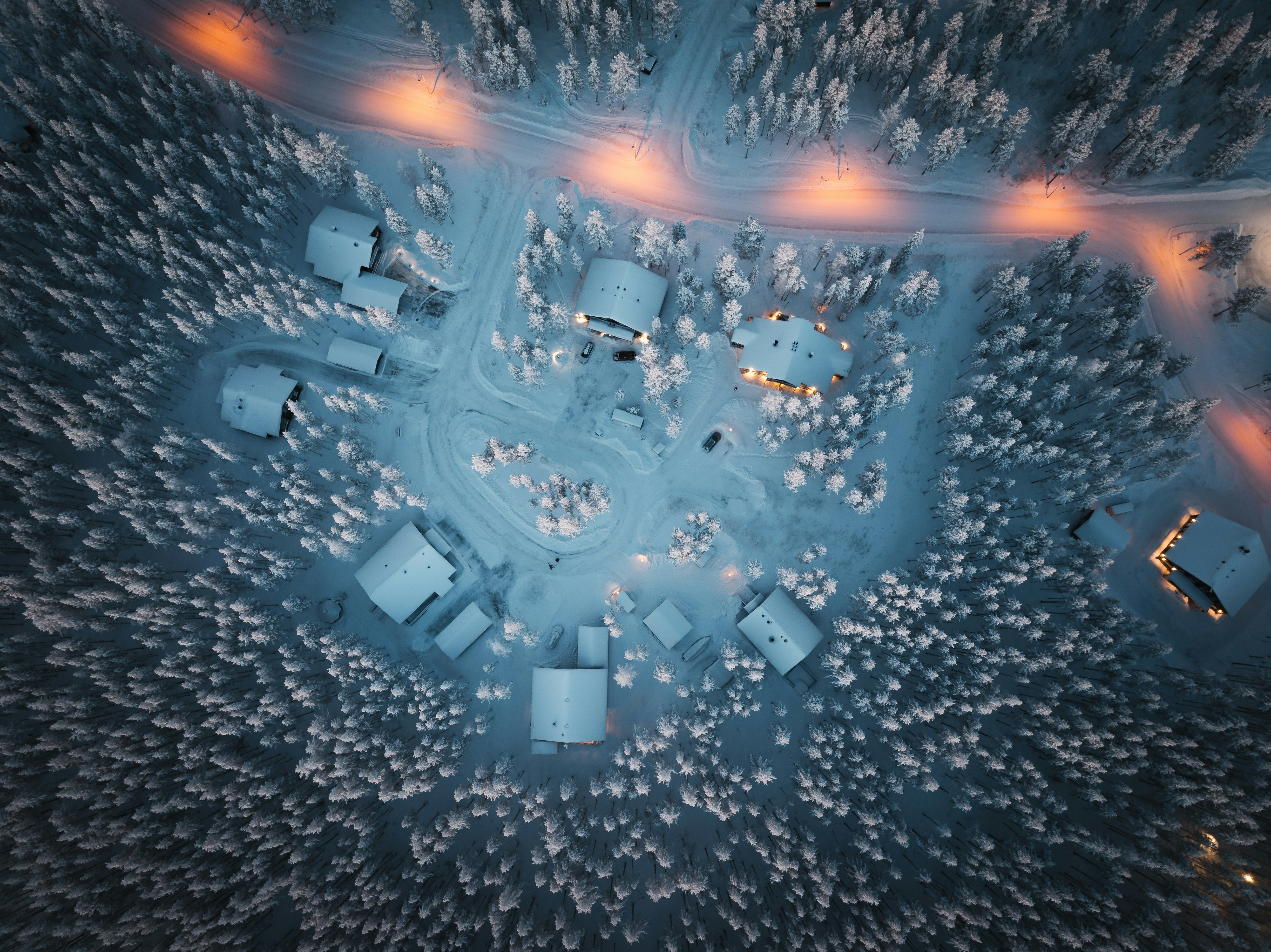 Snow-dusted cabins nestled among frosted trees with warm streetlights casting a glowing contrast.