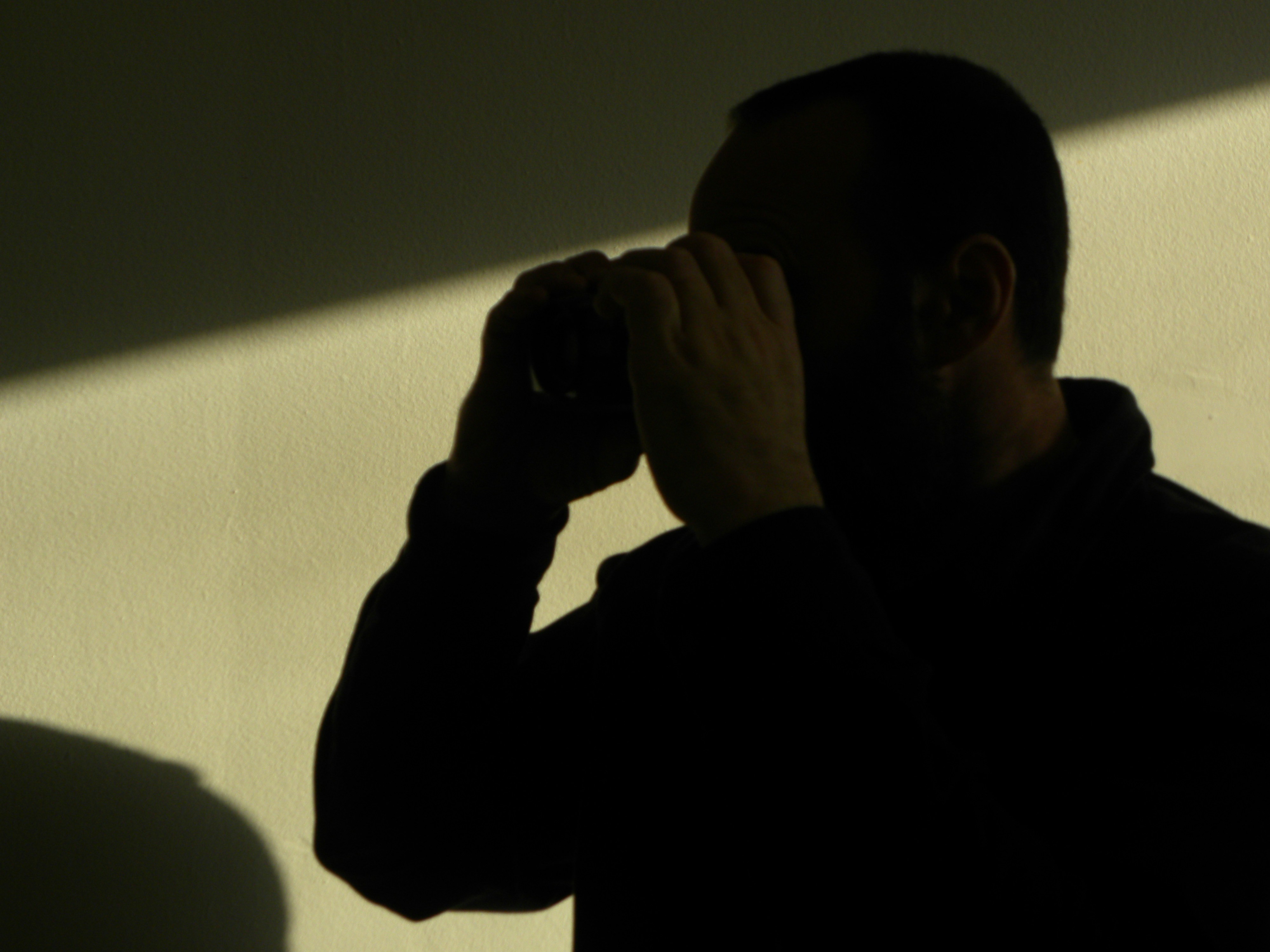 Silhouette of a person holding an object against a softly lit wall, creating a dramatic contrast with shadows.