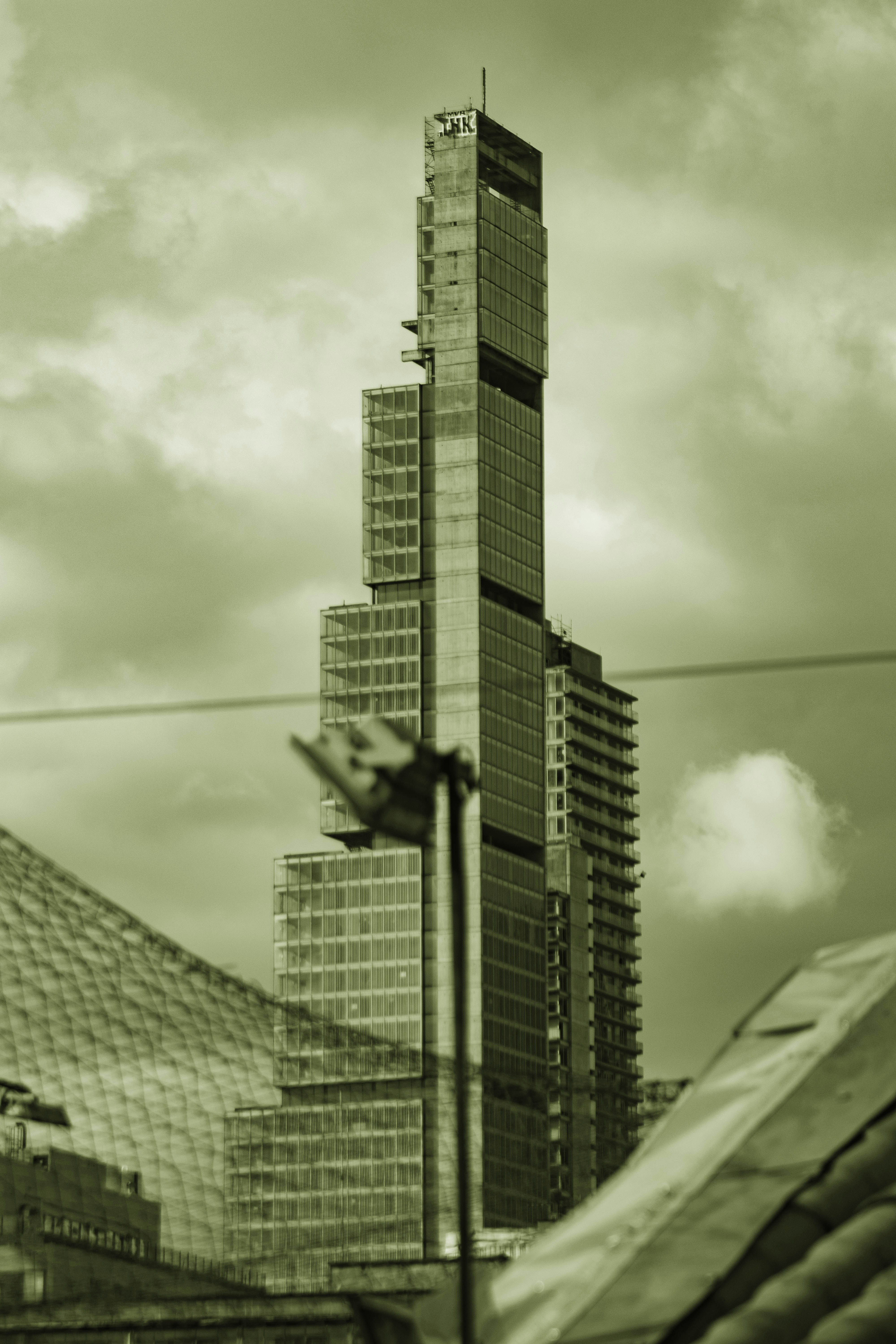 Emerald Vertical: A Segmented Skyscraper Rises Through the Cloudy City