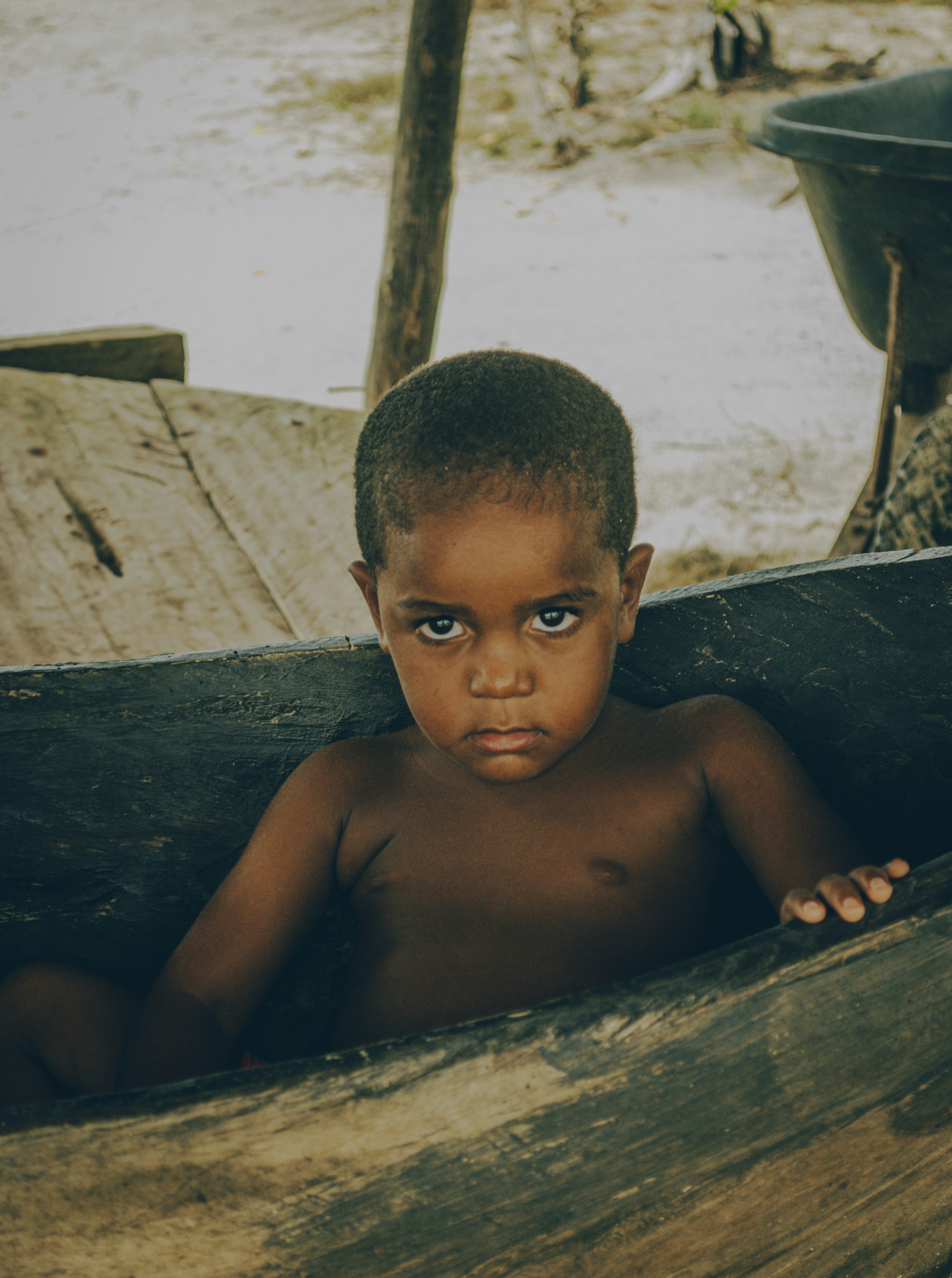 Child sitting in a rustic wooden canoe with a thoughtful expression, surrounded by earthy tones and natural textures.