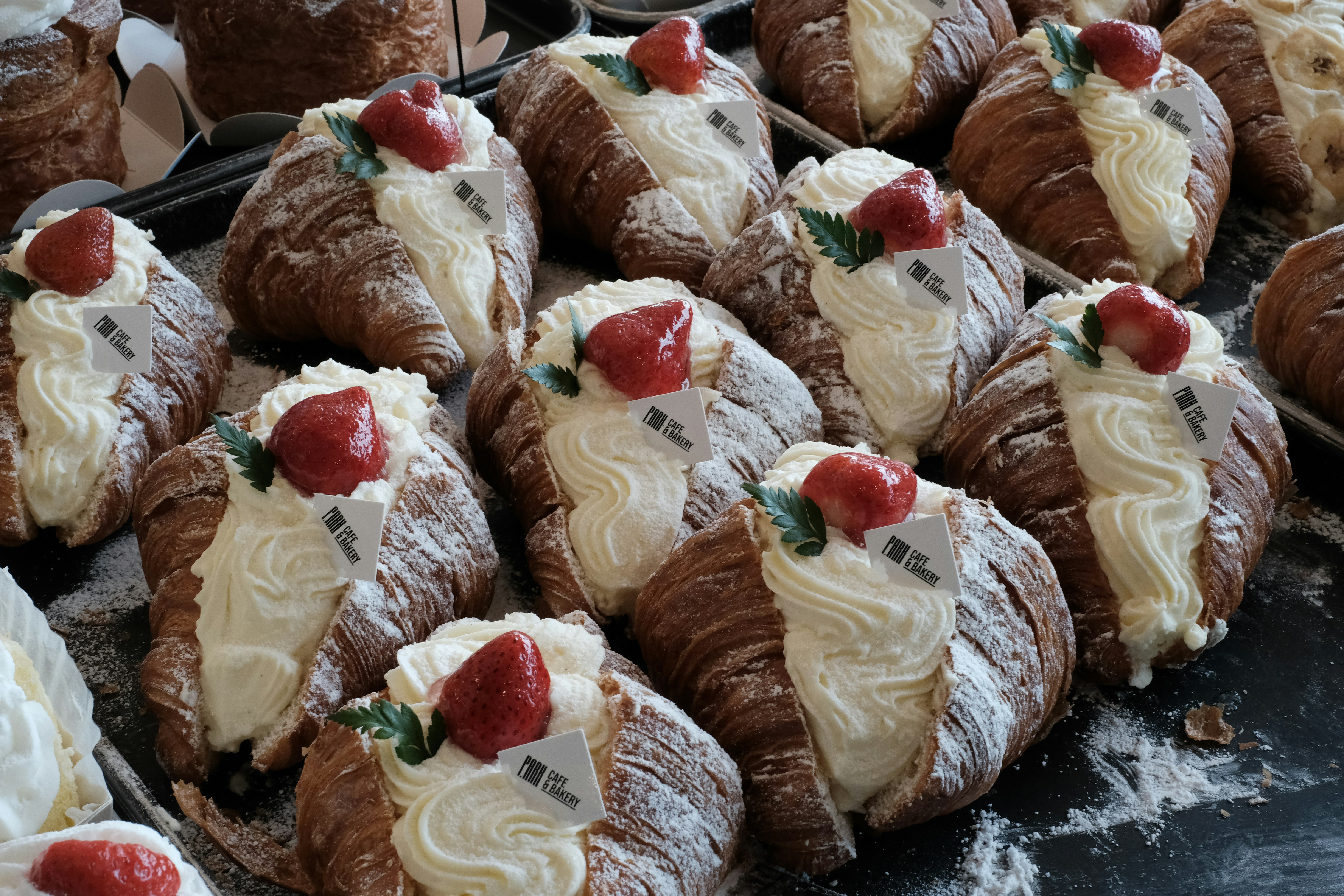 Rows of Cream-Topped Croissants with Strawberry Garnish on a Bakery Tray
