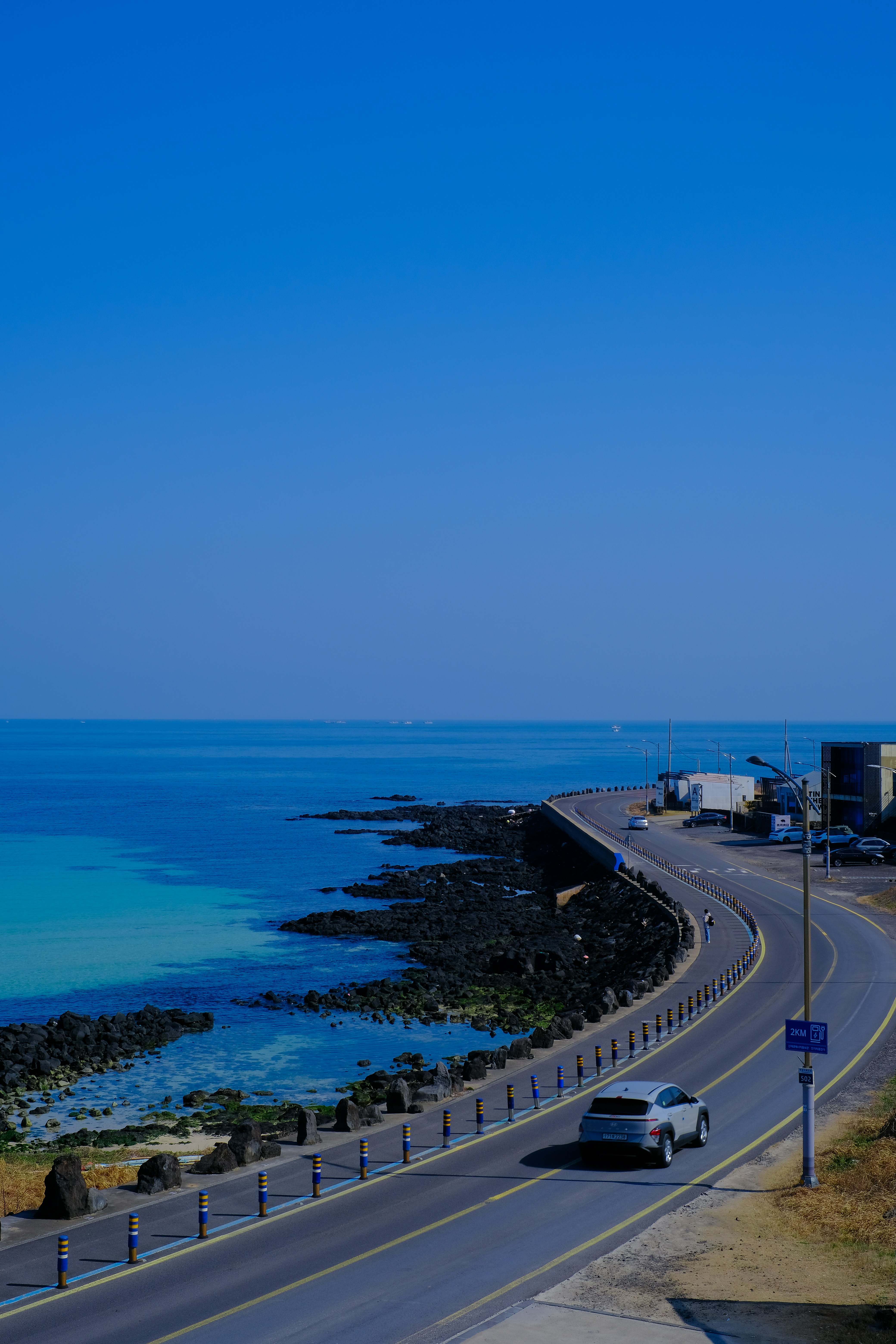 Azure Curve: A Lone Car Traces the Sea-Worn Highway