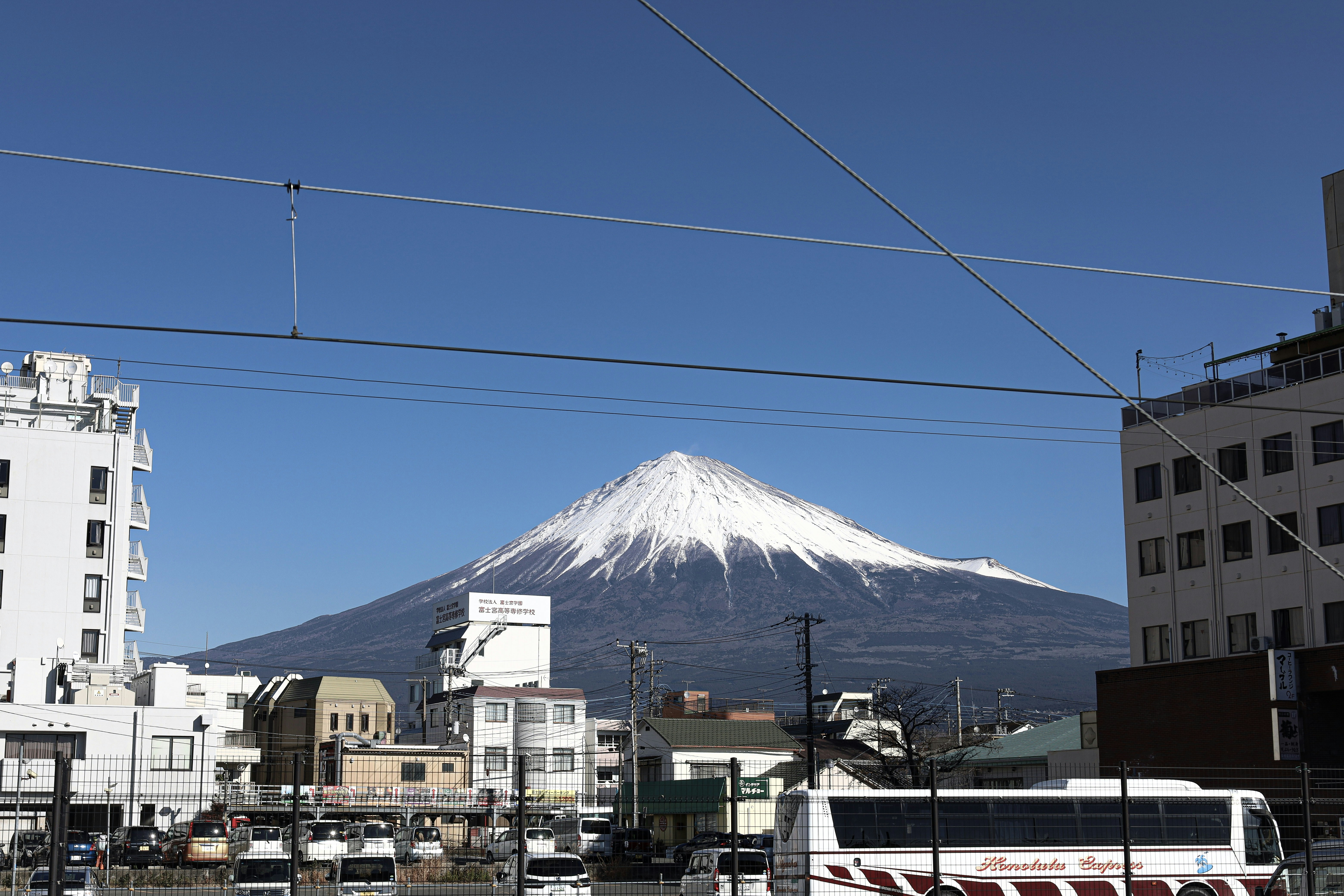 Mount Fuji's snow-capped peak rises behind city buildings under a clear blue sky.