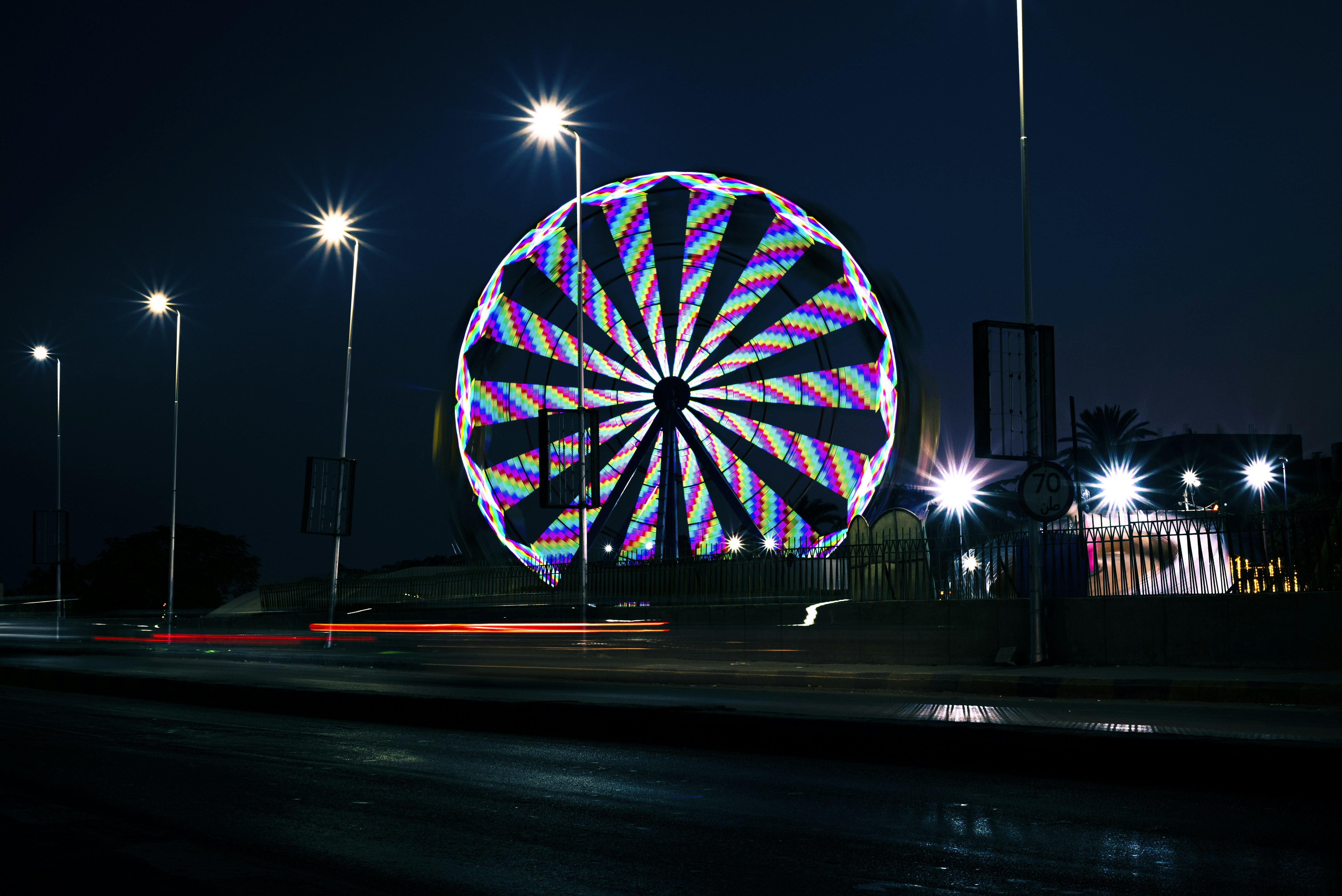 Nocturnal Ferris Wheel: Neon Spokes Bleed Color Across a Quiet Street